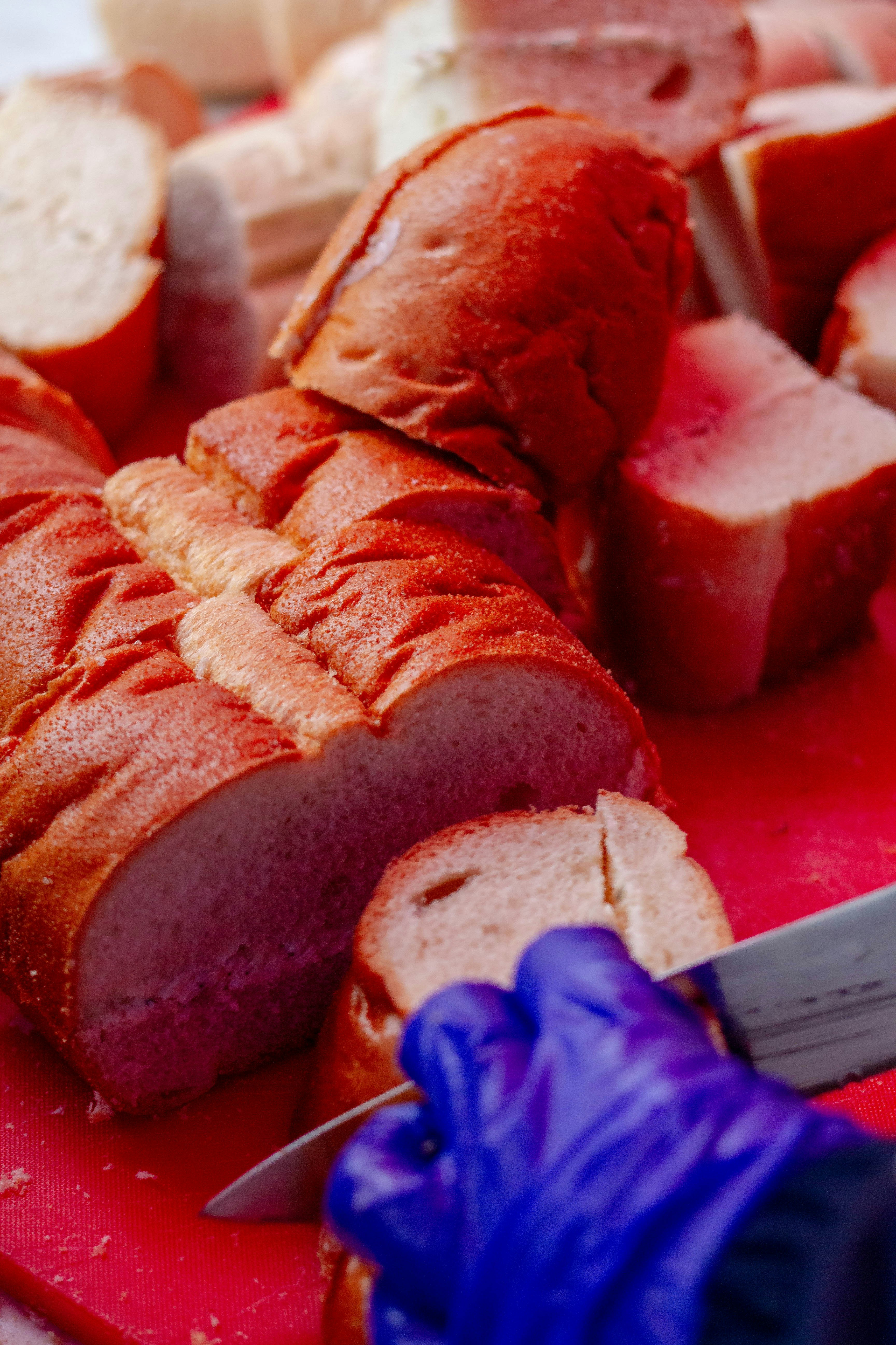 Sliced loafs on a red cutting board as a gloved hand carves a crusty loaf