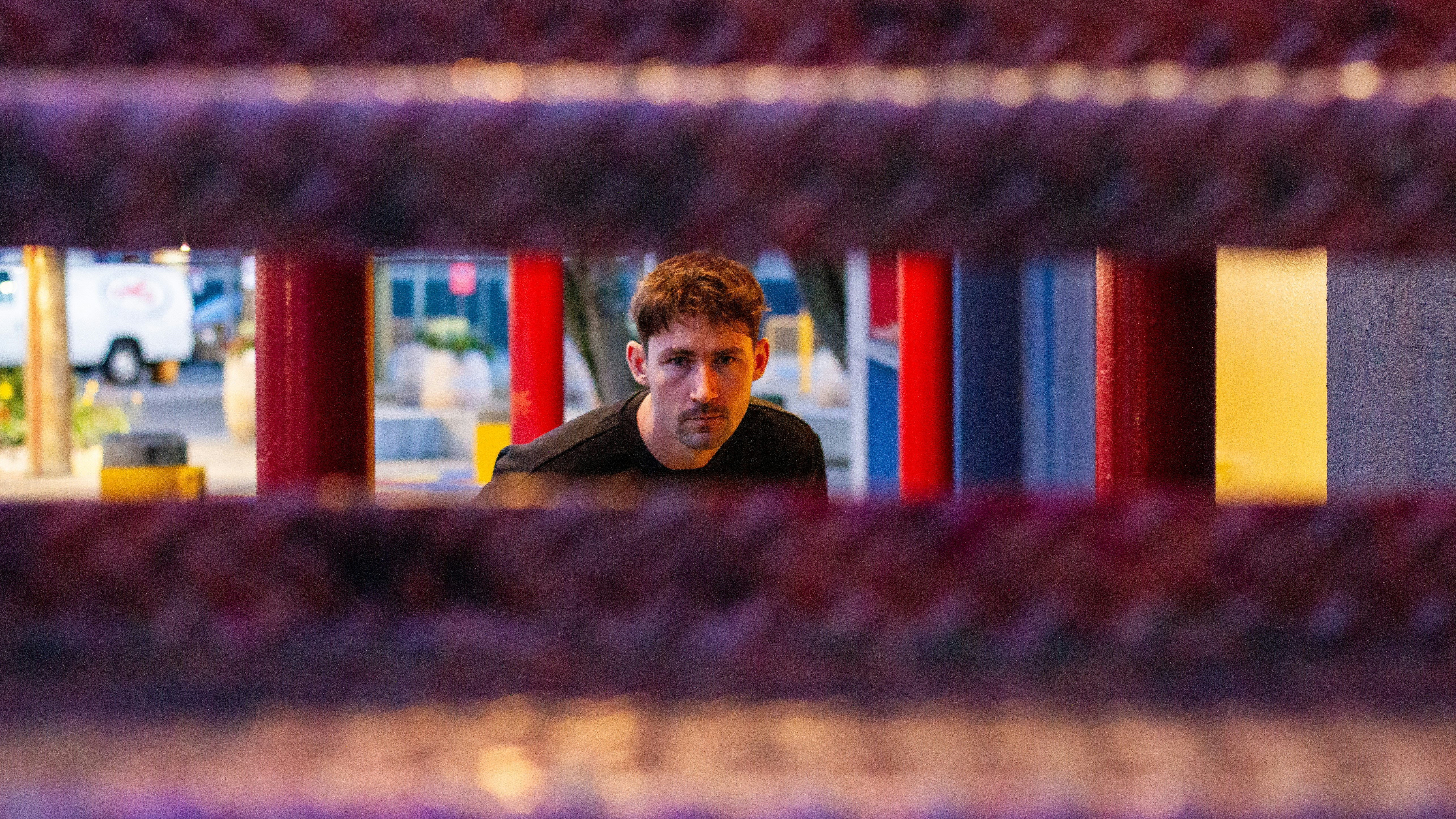 Through the Gaps: A Far-Store Face Framed in Playground Rails