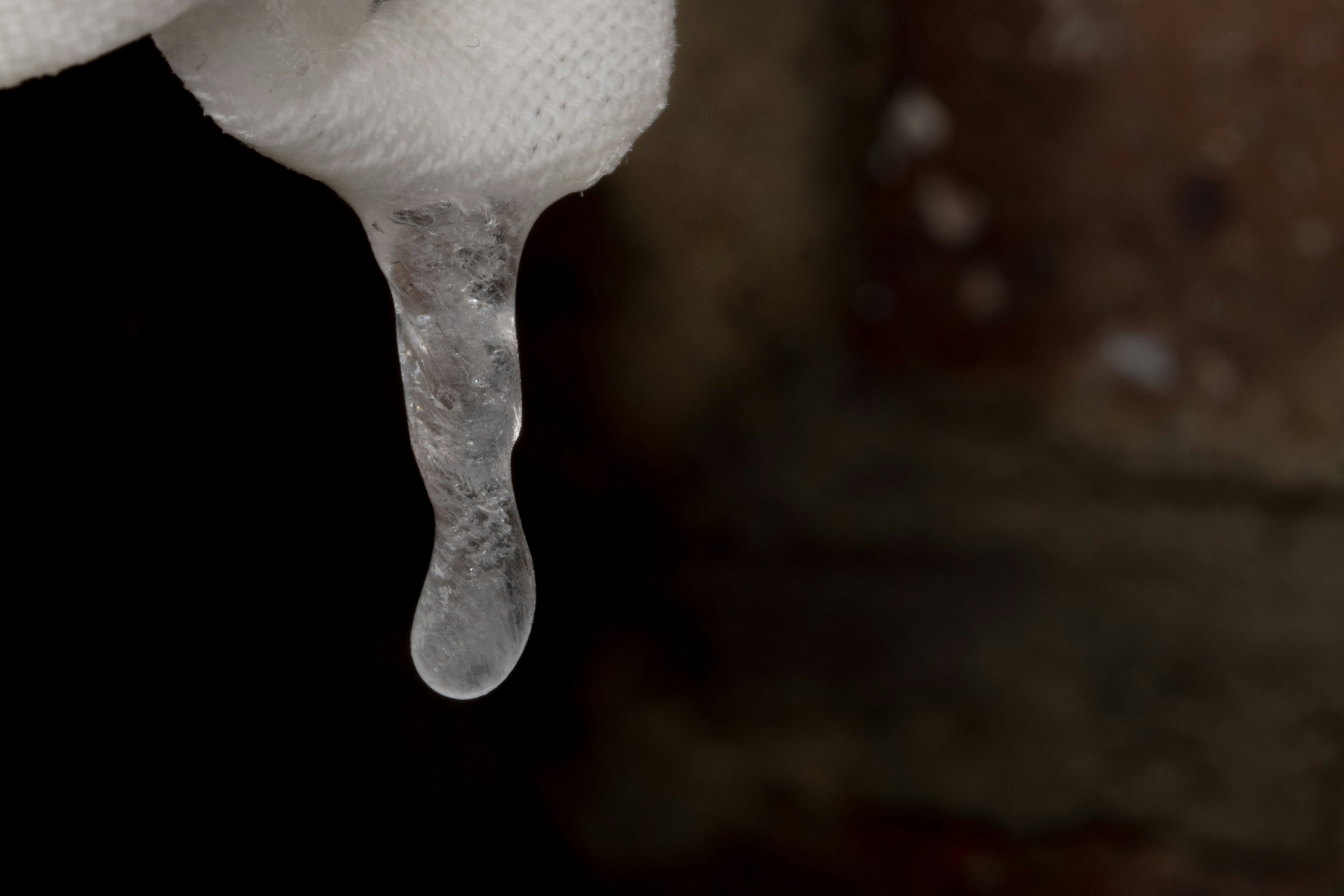 A lone icicle drips from a gloved edge into shadowed darkness