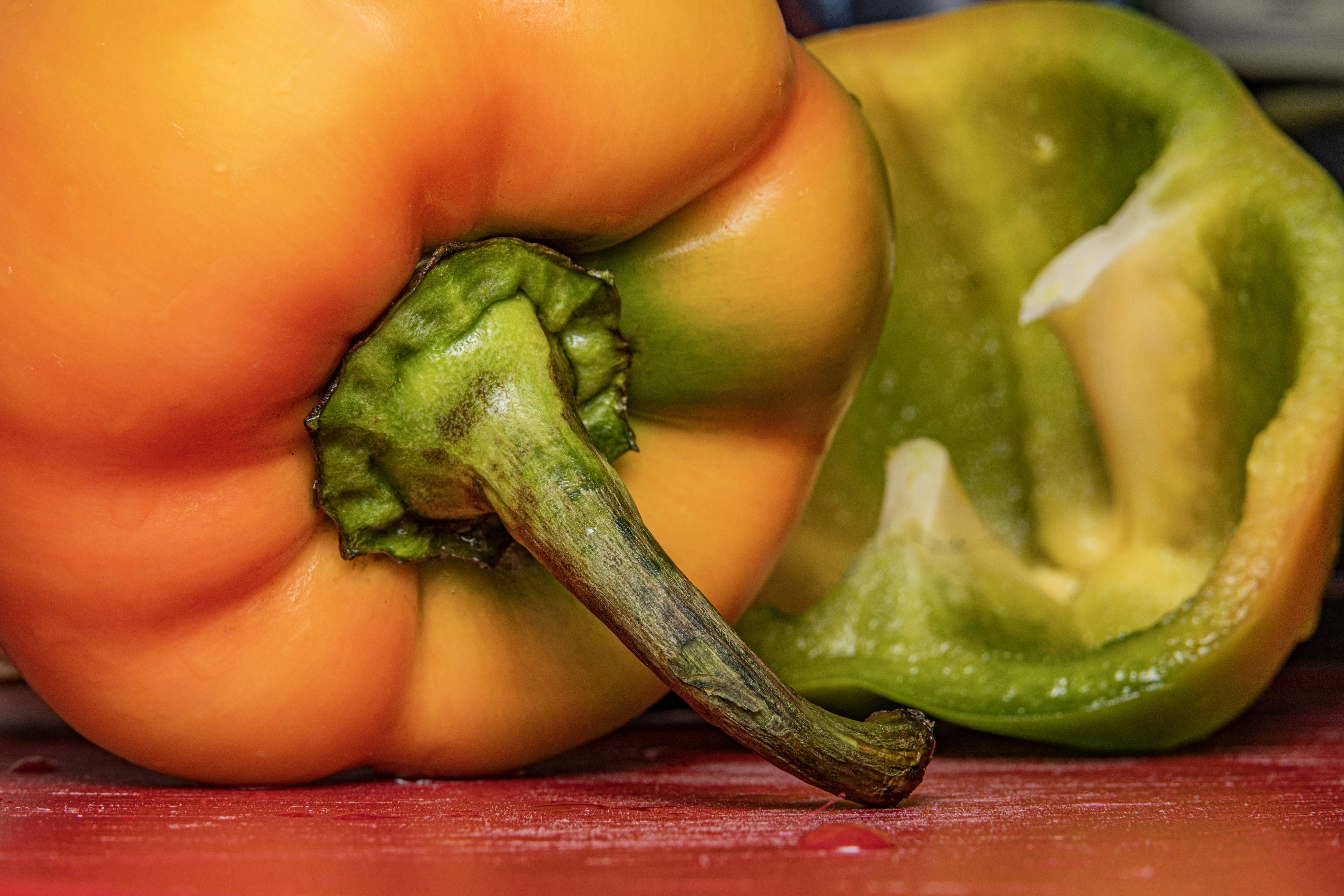 Orange Pepper Crowned with Green Stem on Red Wooden Surface