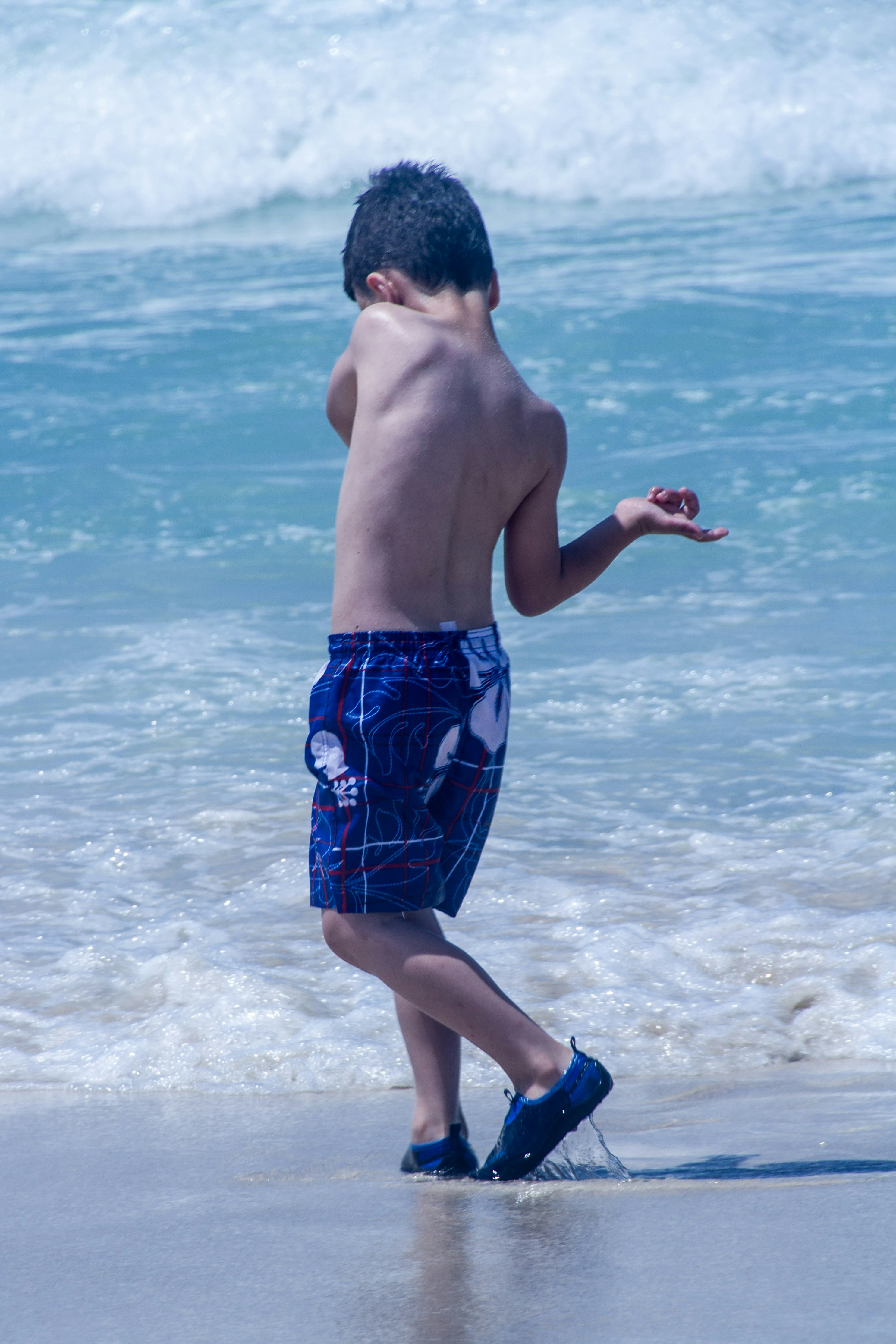 Child in blue swim shorts dances at the edge of rolling waves