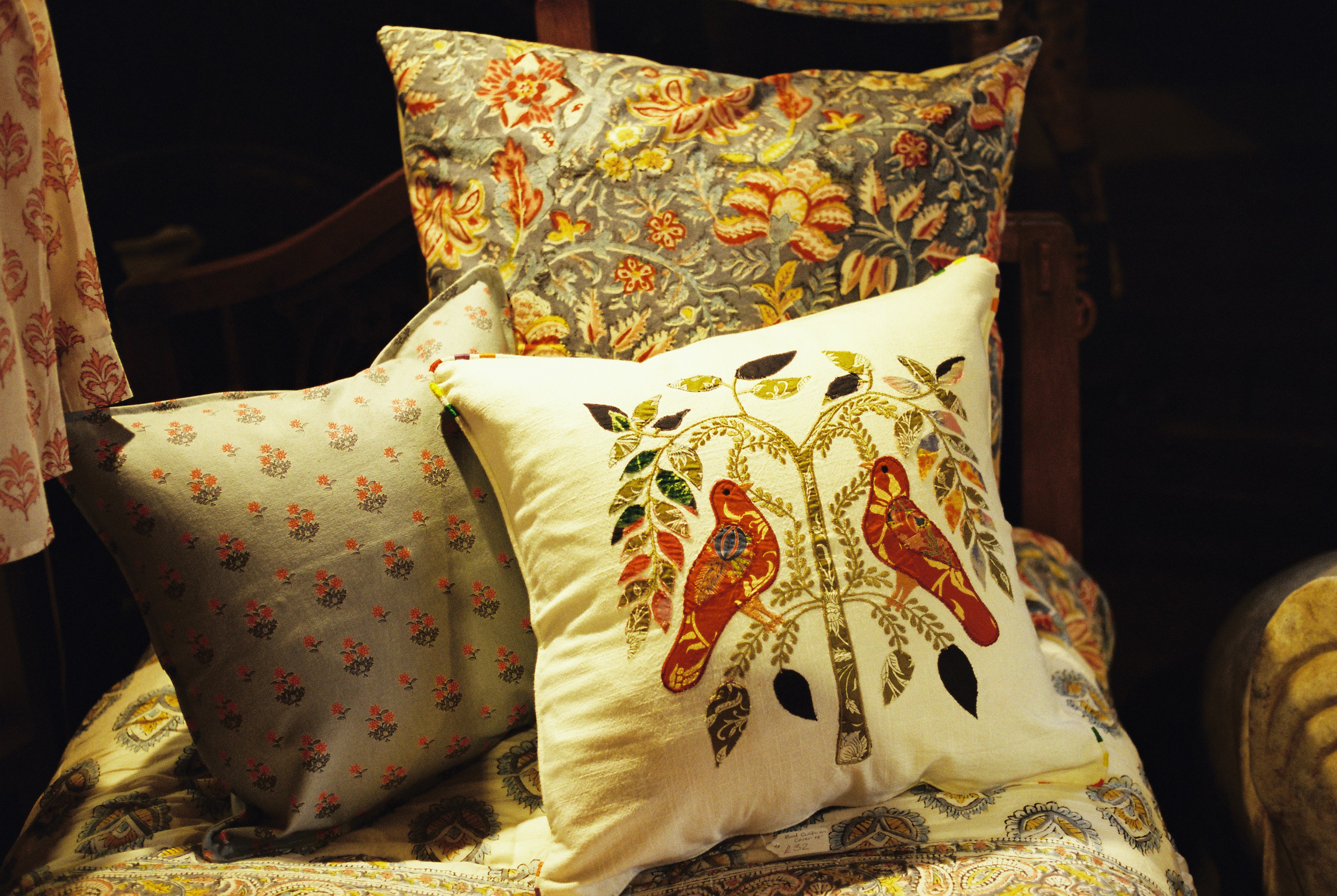 Two decorative cushions with intricate bird-branch embroidery sit atop a patterned quilted chair, forming a warm, textile-rich vignette.