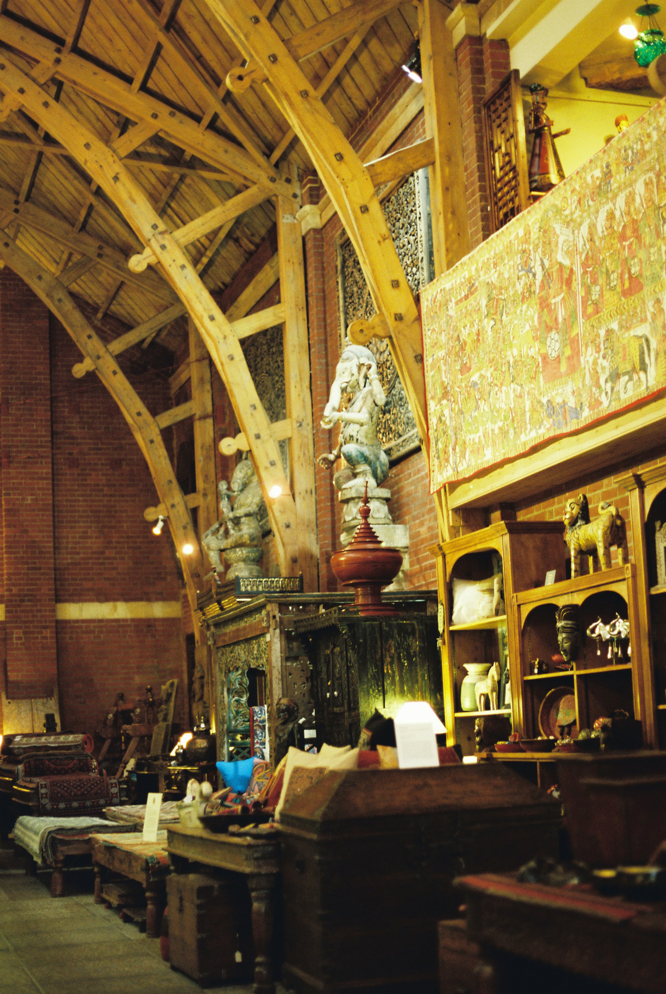 Interior of a warm, arched wooden hall filled with statues, artifacts, and shelves of objects; a cozy, museum-like display scene with vintage decor.