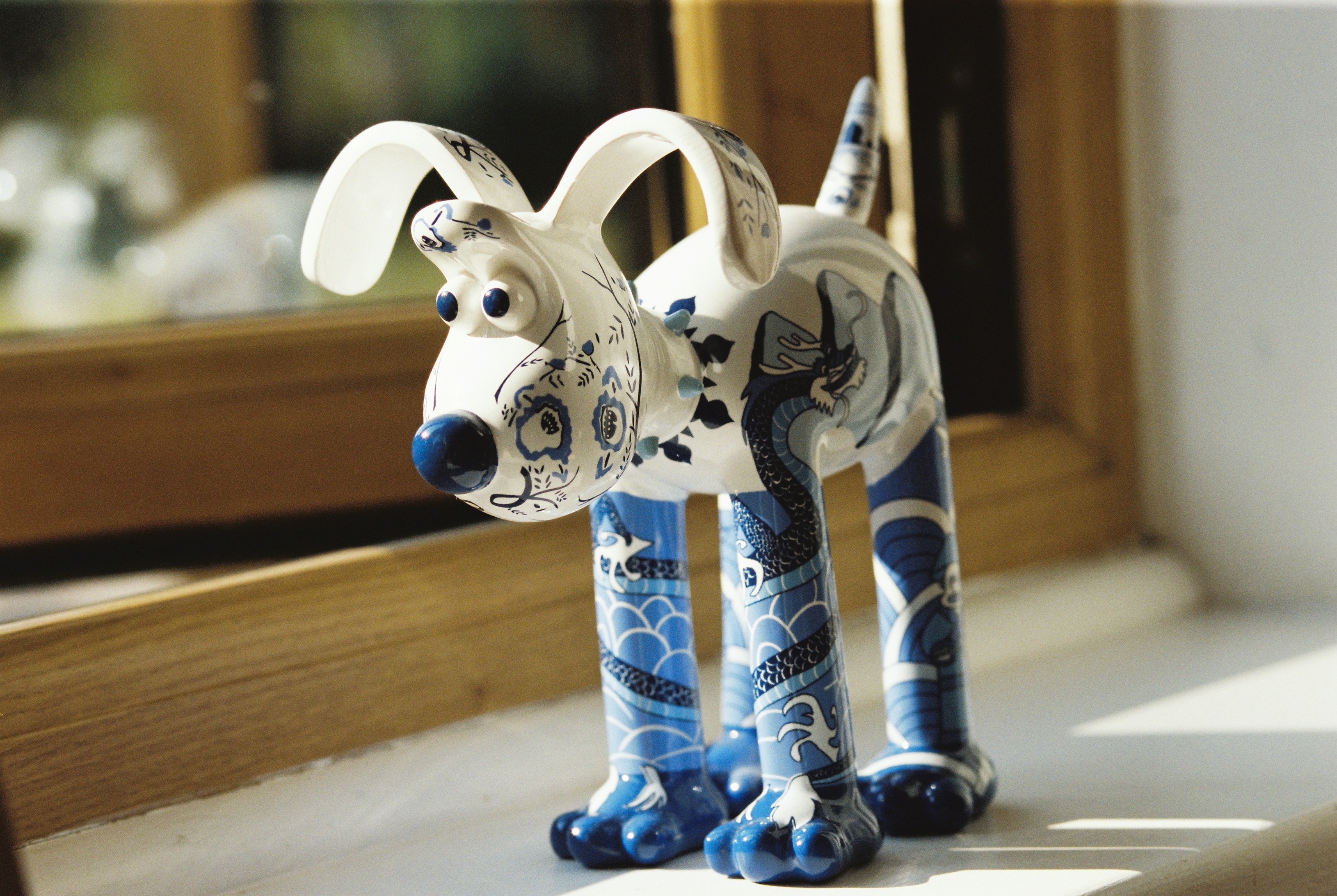 Ceramic blue-and-white dog sculpture perched on a sunlit windowsill, details and shadows emphasized by natural light.