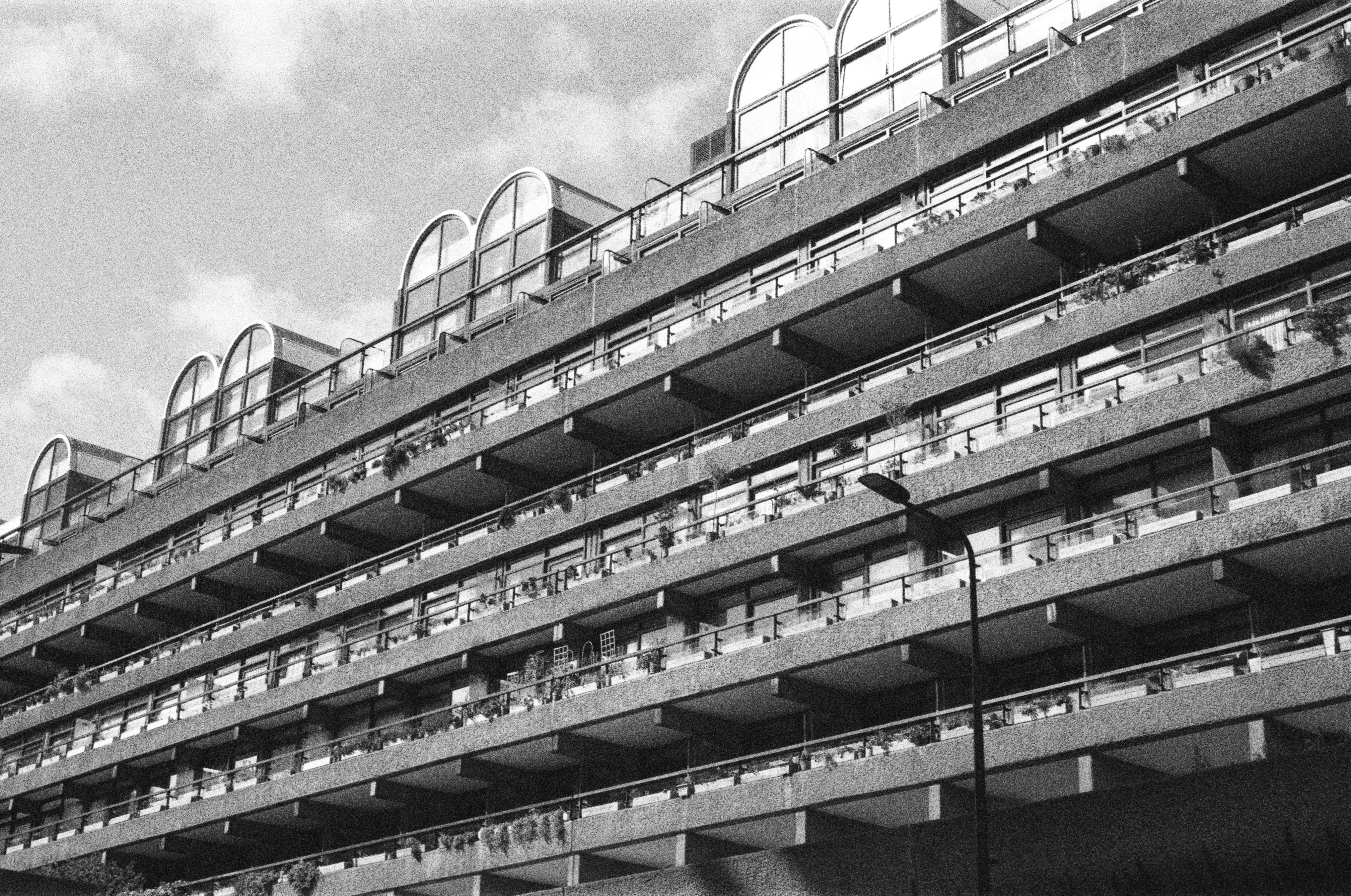 Monochrome shot of a multi-level apartment building with repetitive balconies and arched skylights, emphasizing geometric rhythm. The scene reads as architectural texture rather than a portrait.
