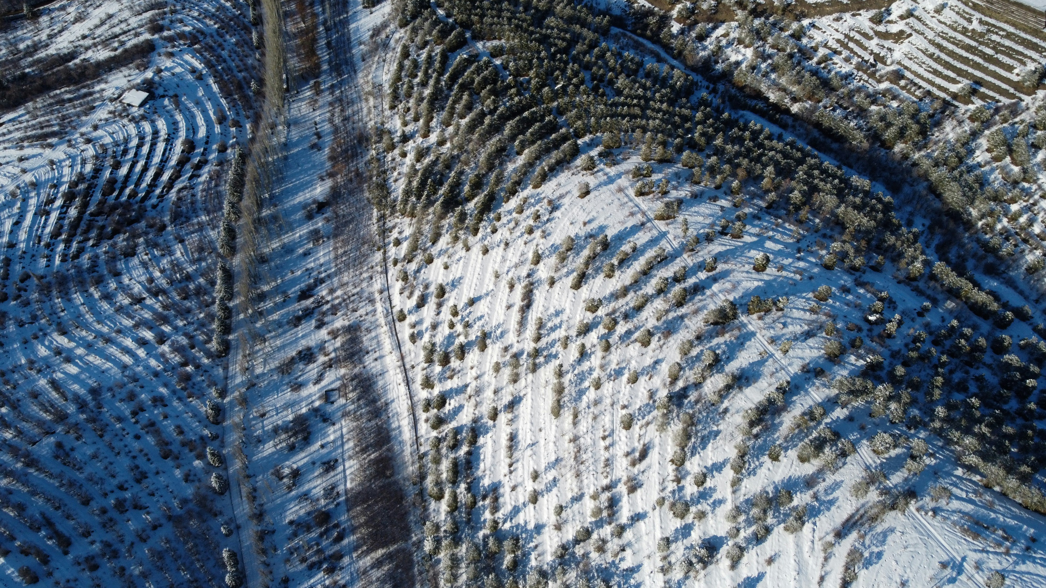 Snow-covered ridges and textured patterns stretch across a frozen landscape, captured from above to emphasize depth and contrast.