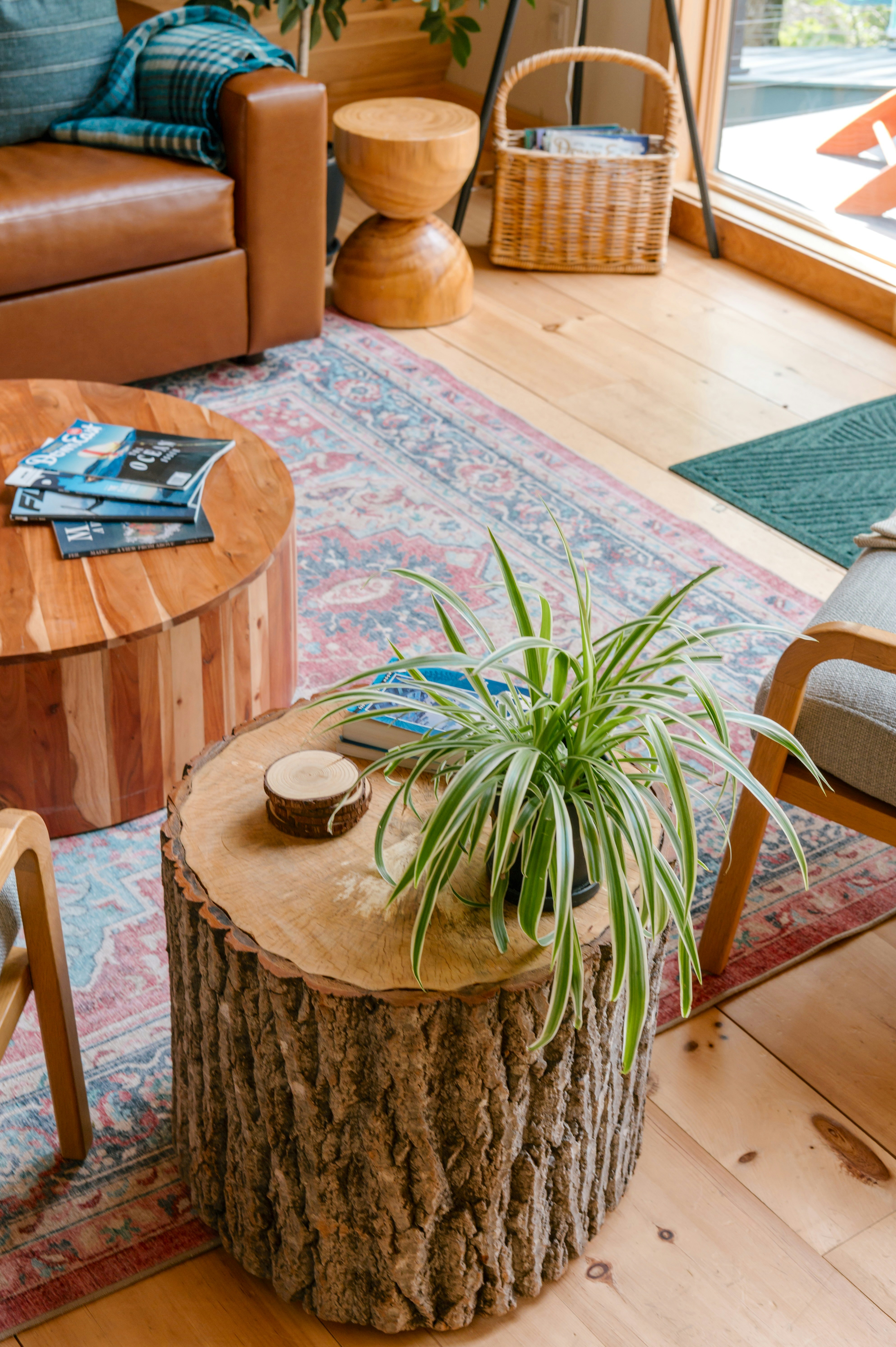 Cozy lounge with a carved tree stump as a side table and a potted plant; warm wood tones, a rug, and a basket near a glass door.