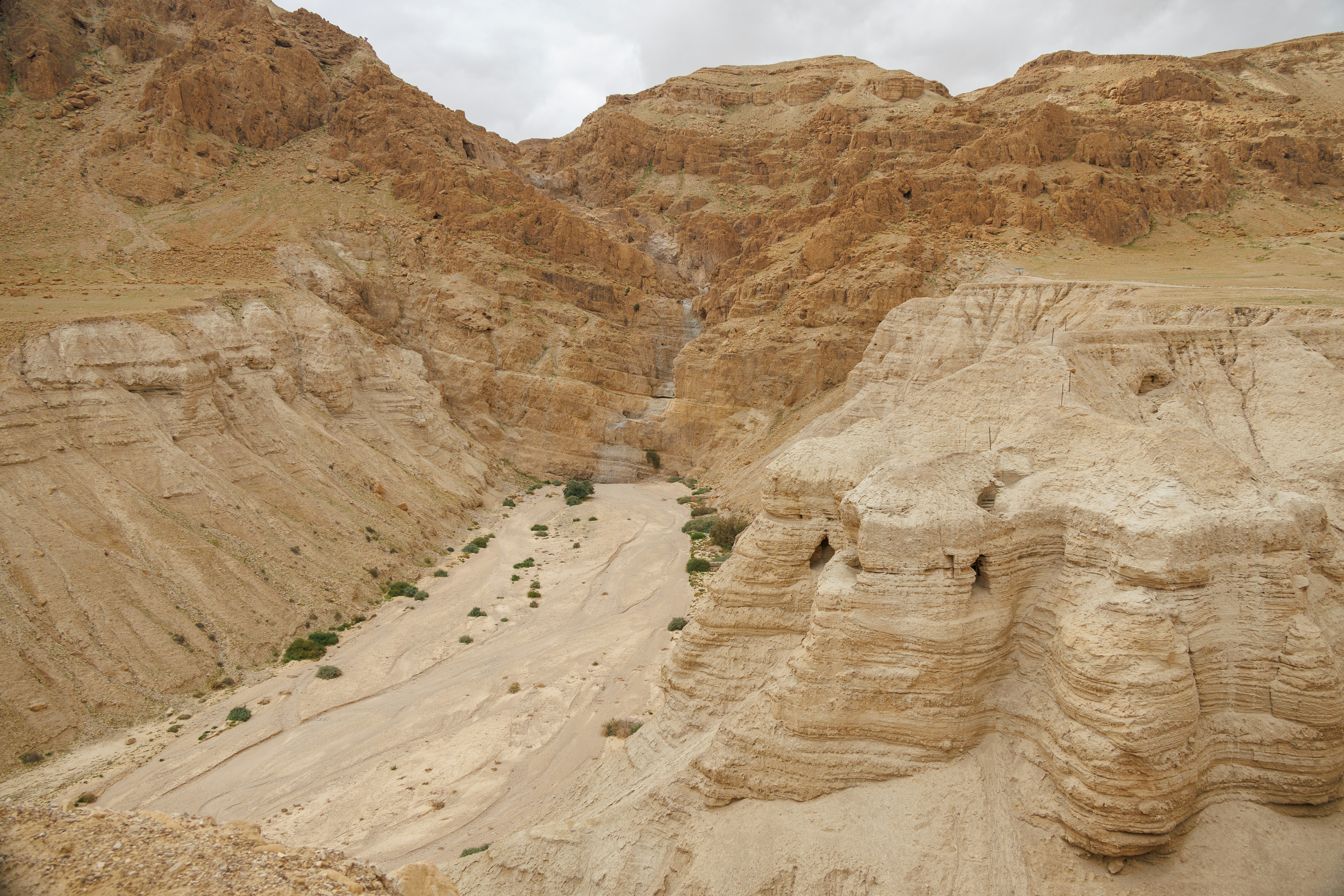 Desert canyon with layered sandstone walls and a dry bed winding through the valley. A stark, arid landscape highlighting natural erosion features and minimal vegetation.