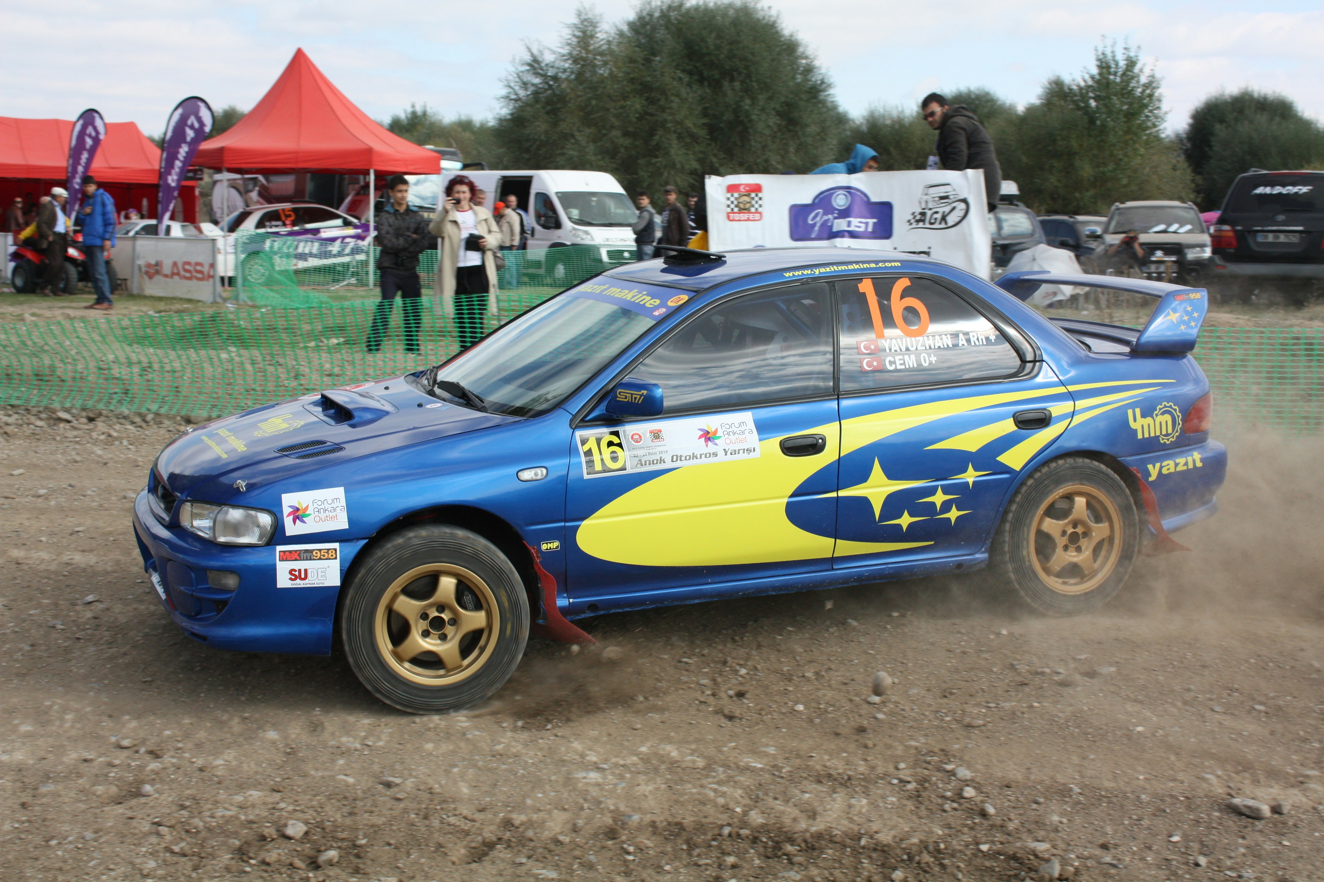Blue rally sentinel: wheel-spray and dust chase on a dirt corner