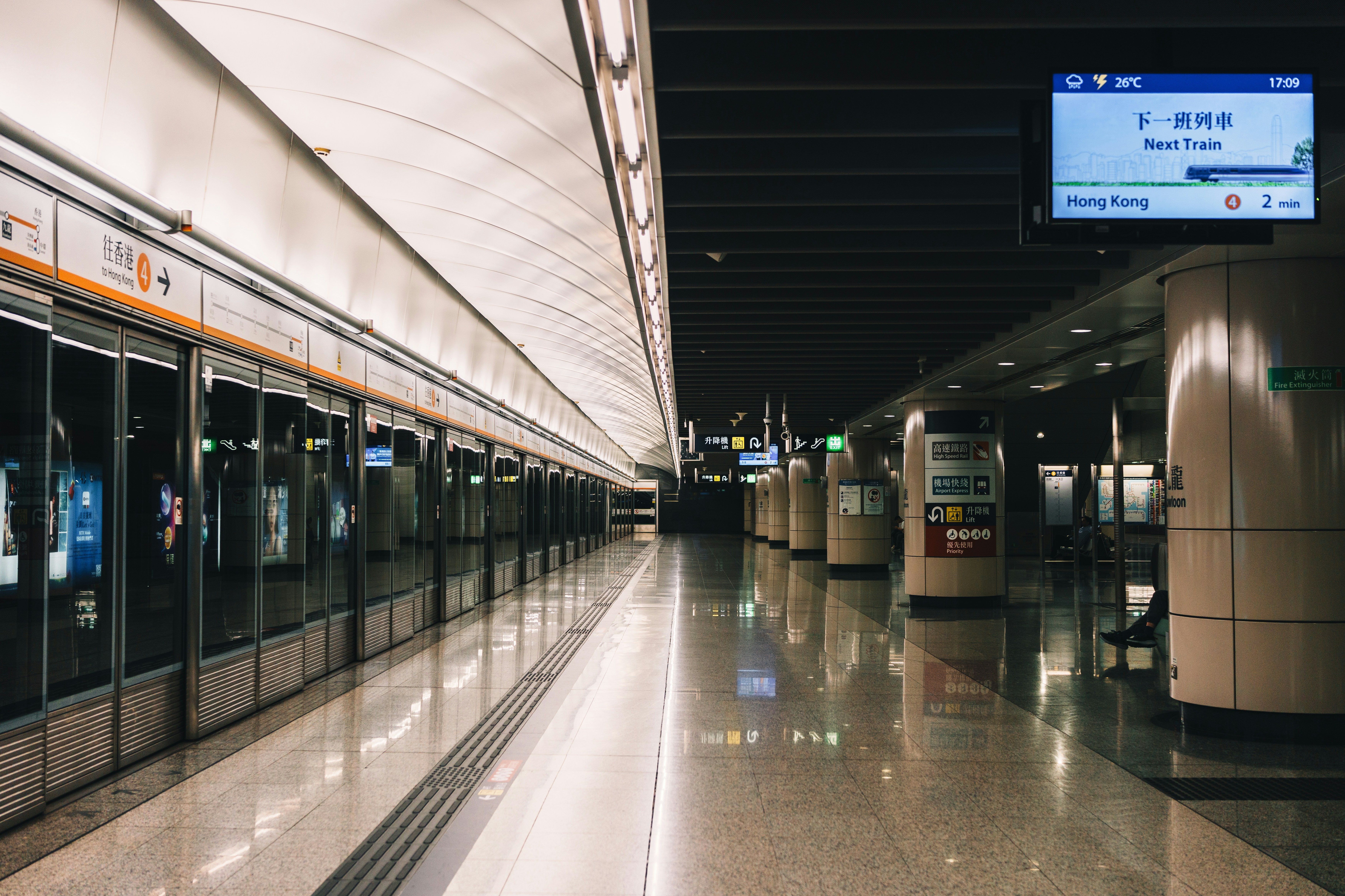 An empty metropolitan subway platform stretches into the distance, with polished floors reflecting overhead lights and glass-walled train cars along the track. A lone, quiet moment in a modern transit hub.