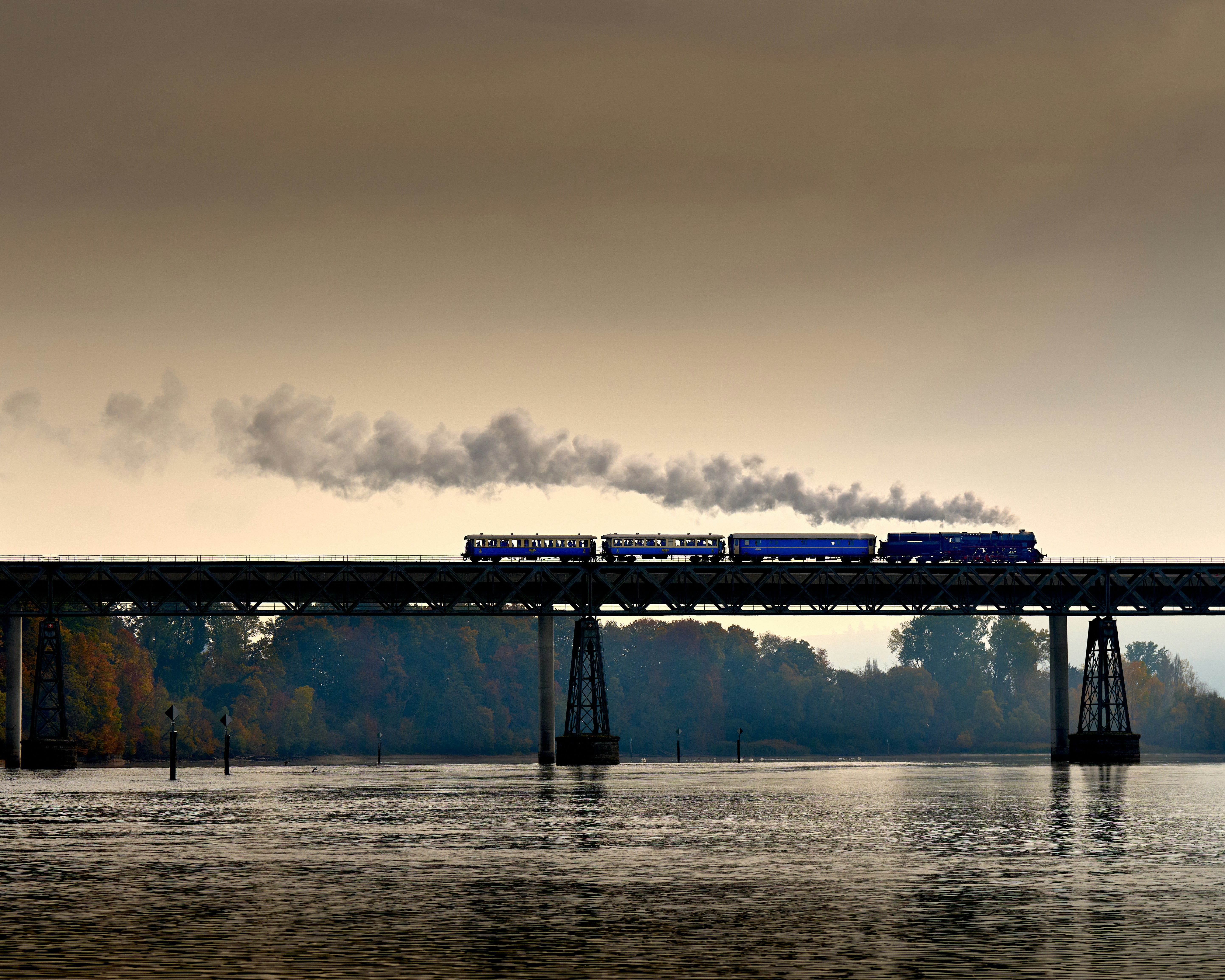 Smoke over steel: a lone steam-train gliding across a river bridge at dusk