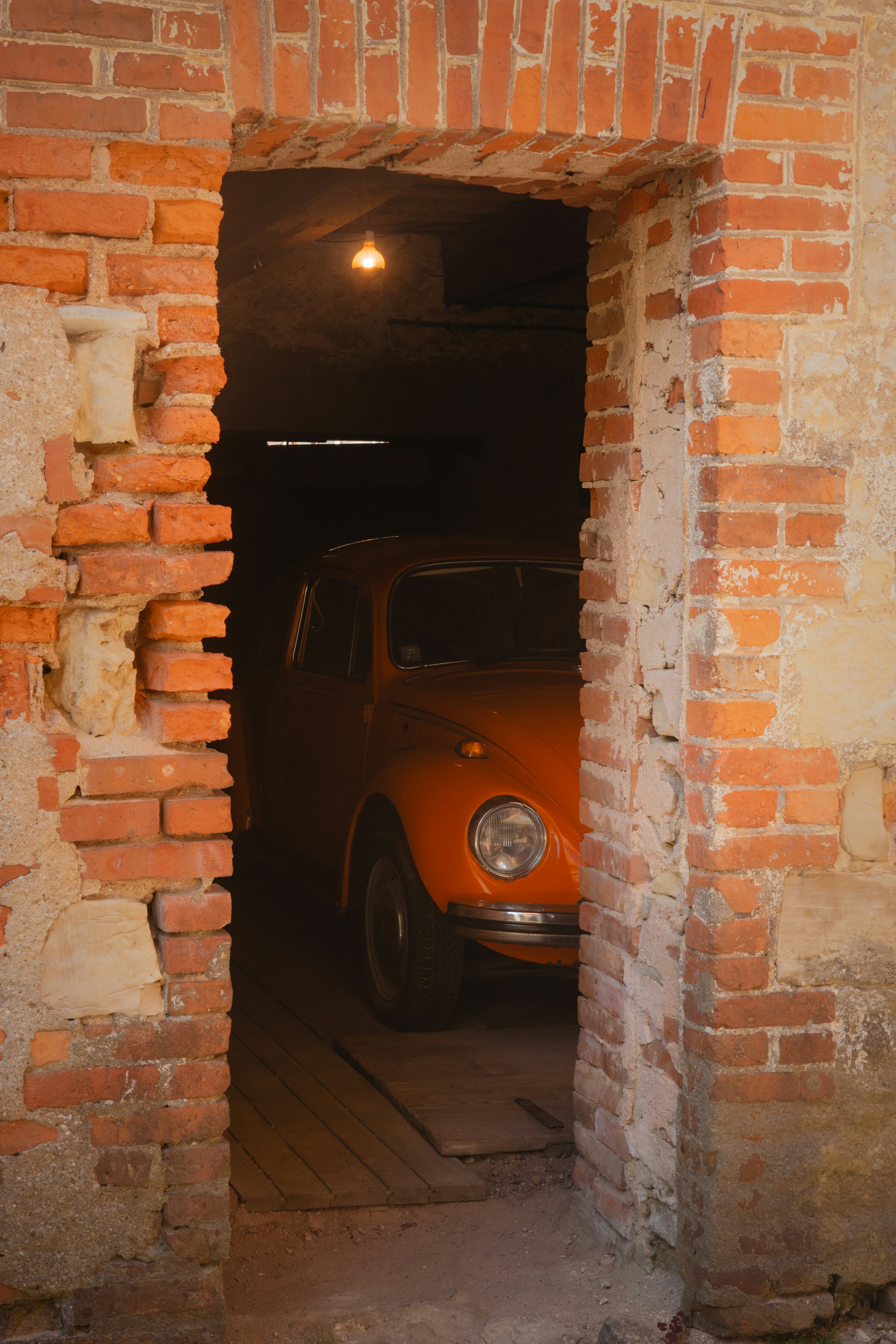 Orange relic in a brick doorway: a vintage car peeks from the shadows