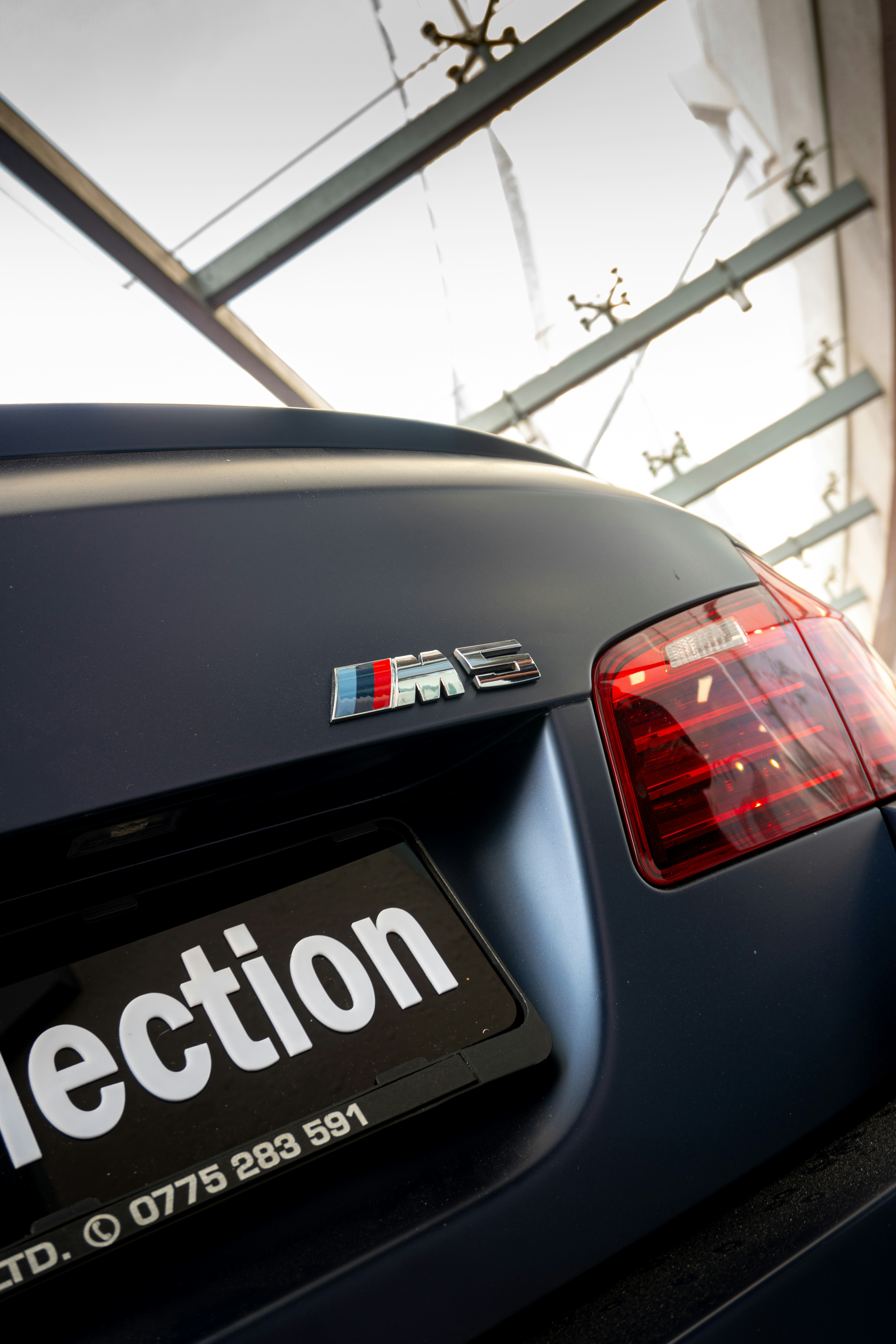 BMW M3 badge and taillight on a dark blue coupe in a modern showroom