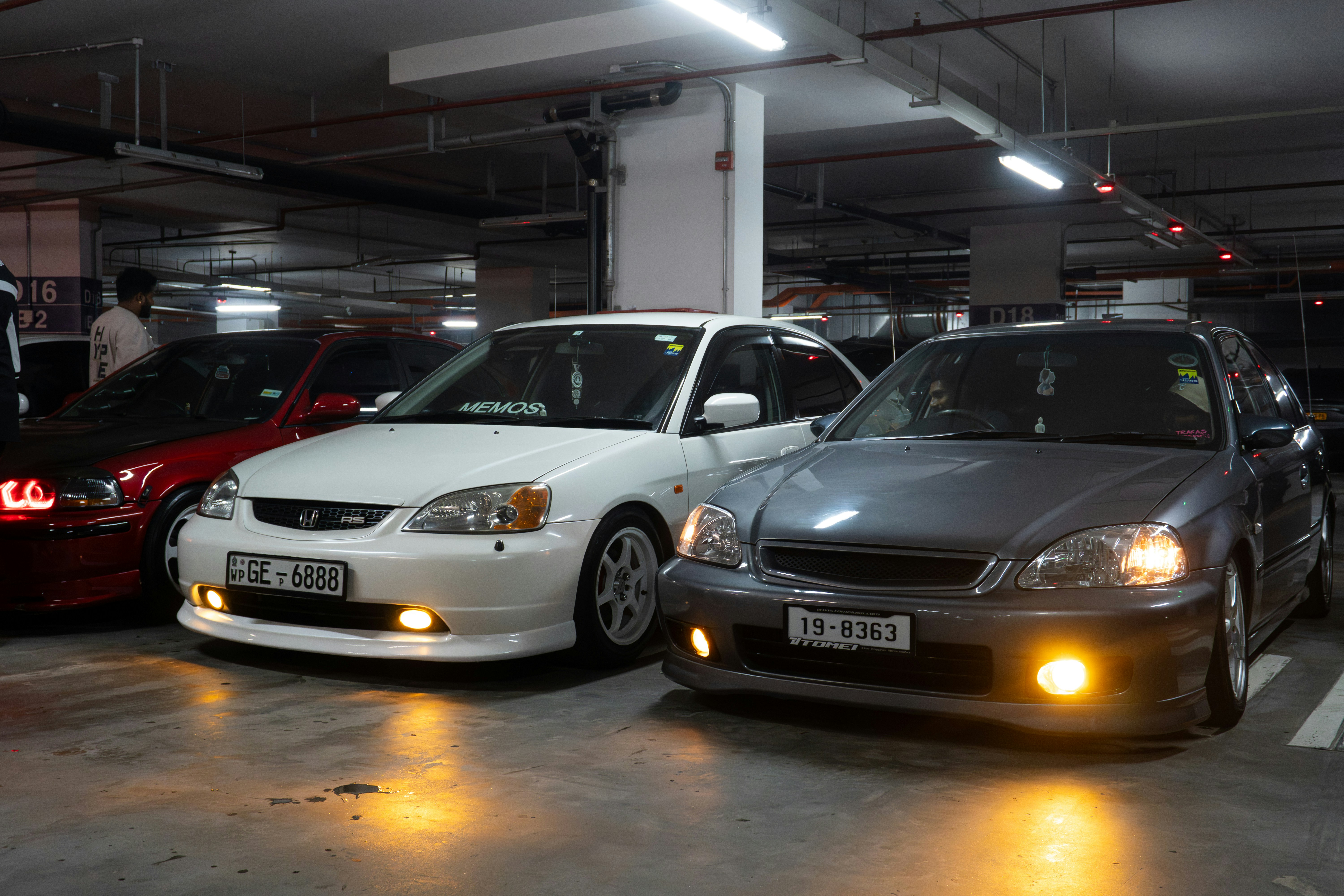 Two compact sedans with glowing headlights in a dim underground parking lot