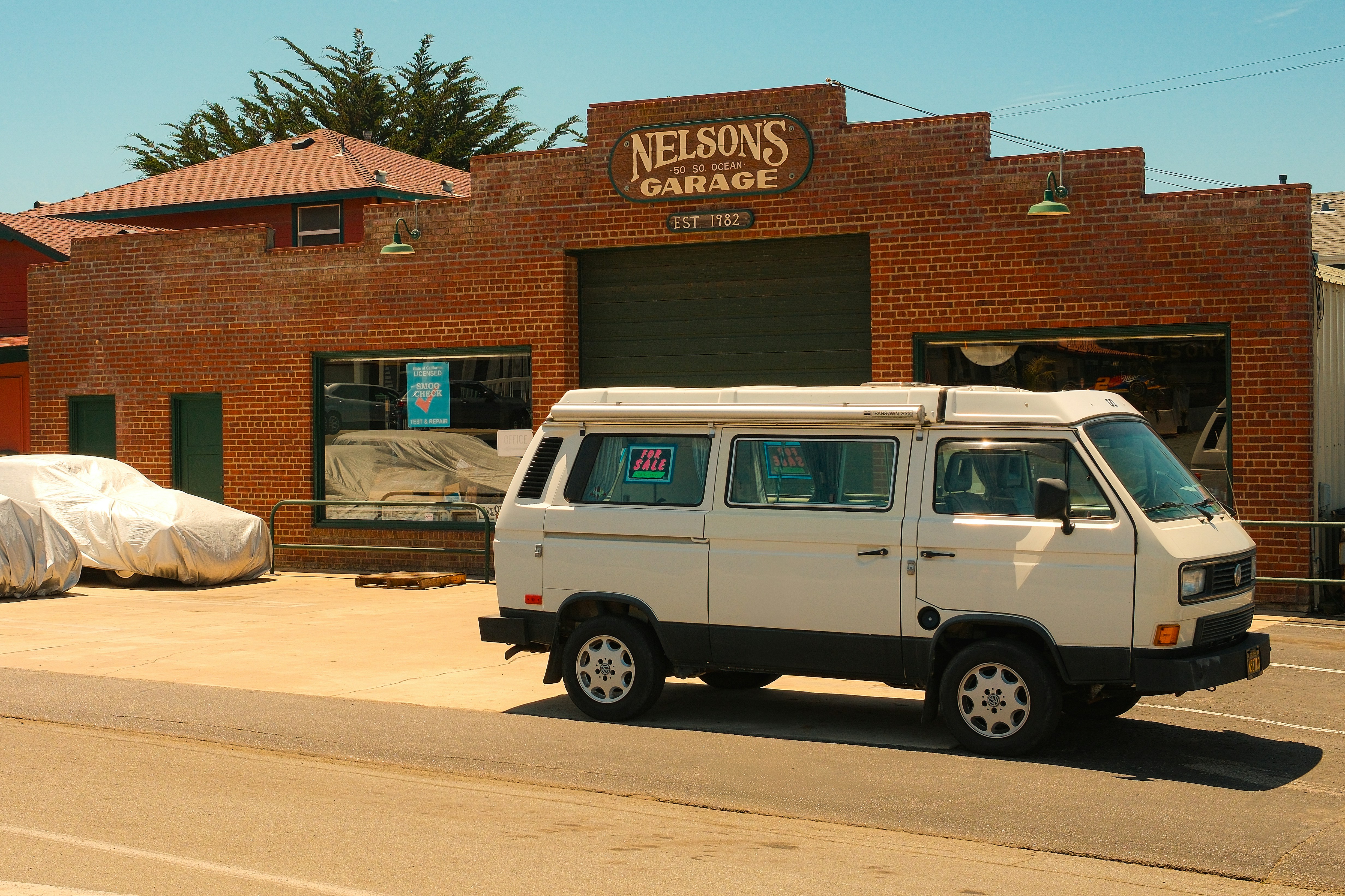 White VW-inspired van rests outside Nelson's Garage in warm daylight