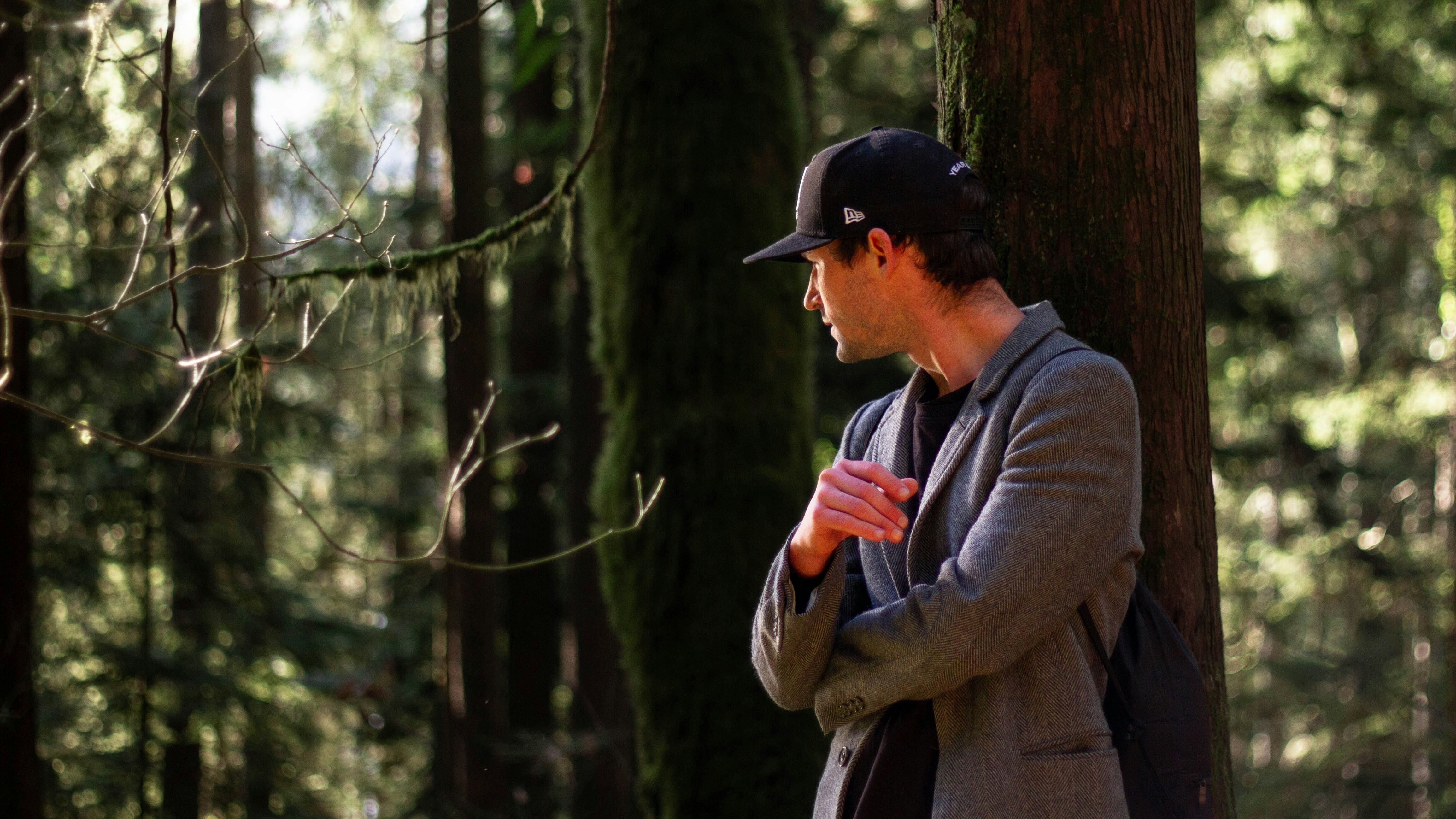 Forest Confidante: A man paused mid-think beside towering trunks