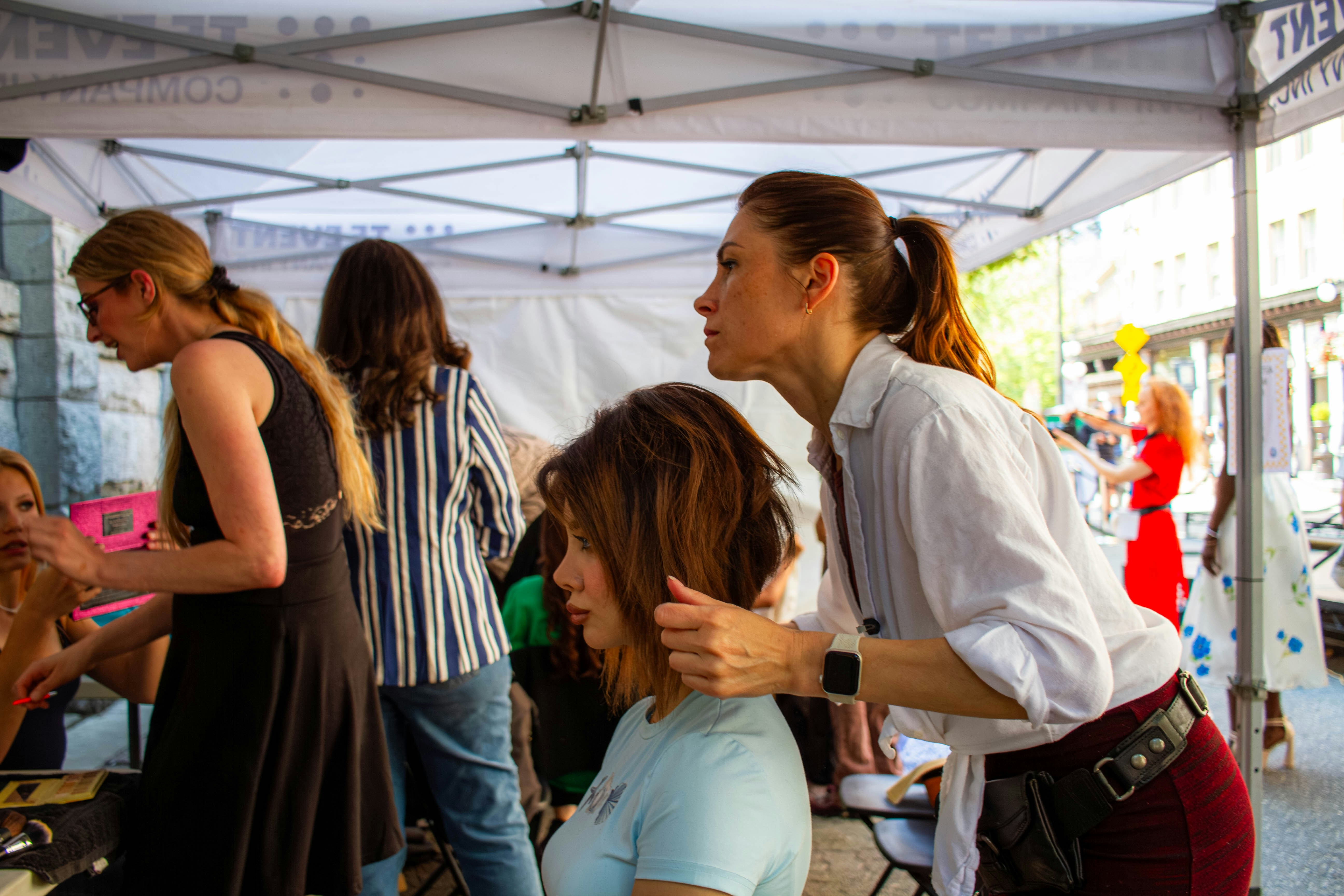 Volunteer in white blouse styles the scene under a canopy as event attendees cluster nearby
