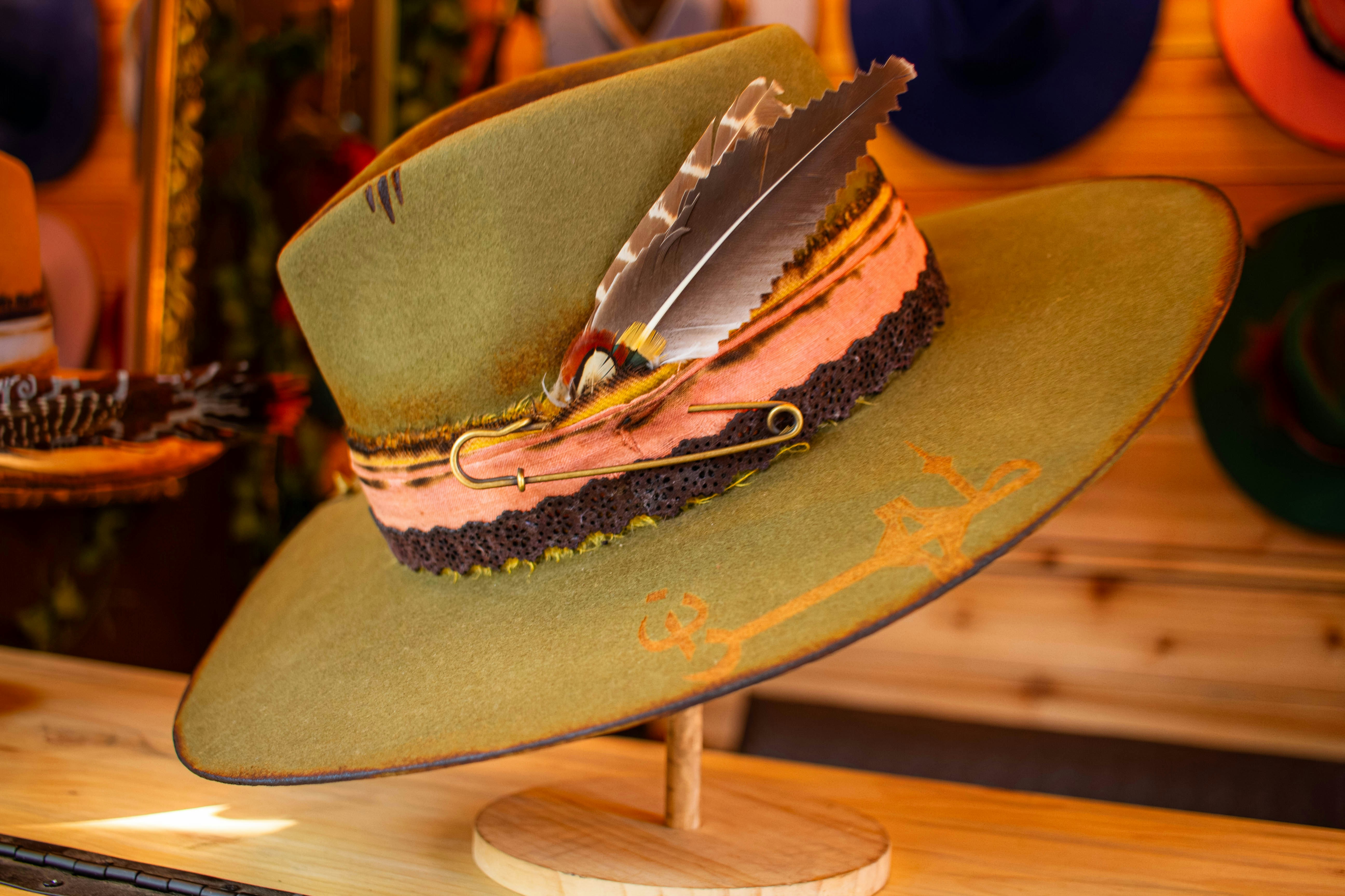 A green felt hat with feathers on a wooden stand.