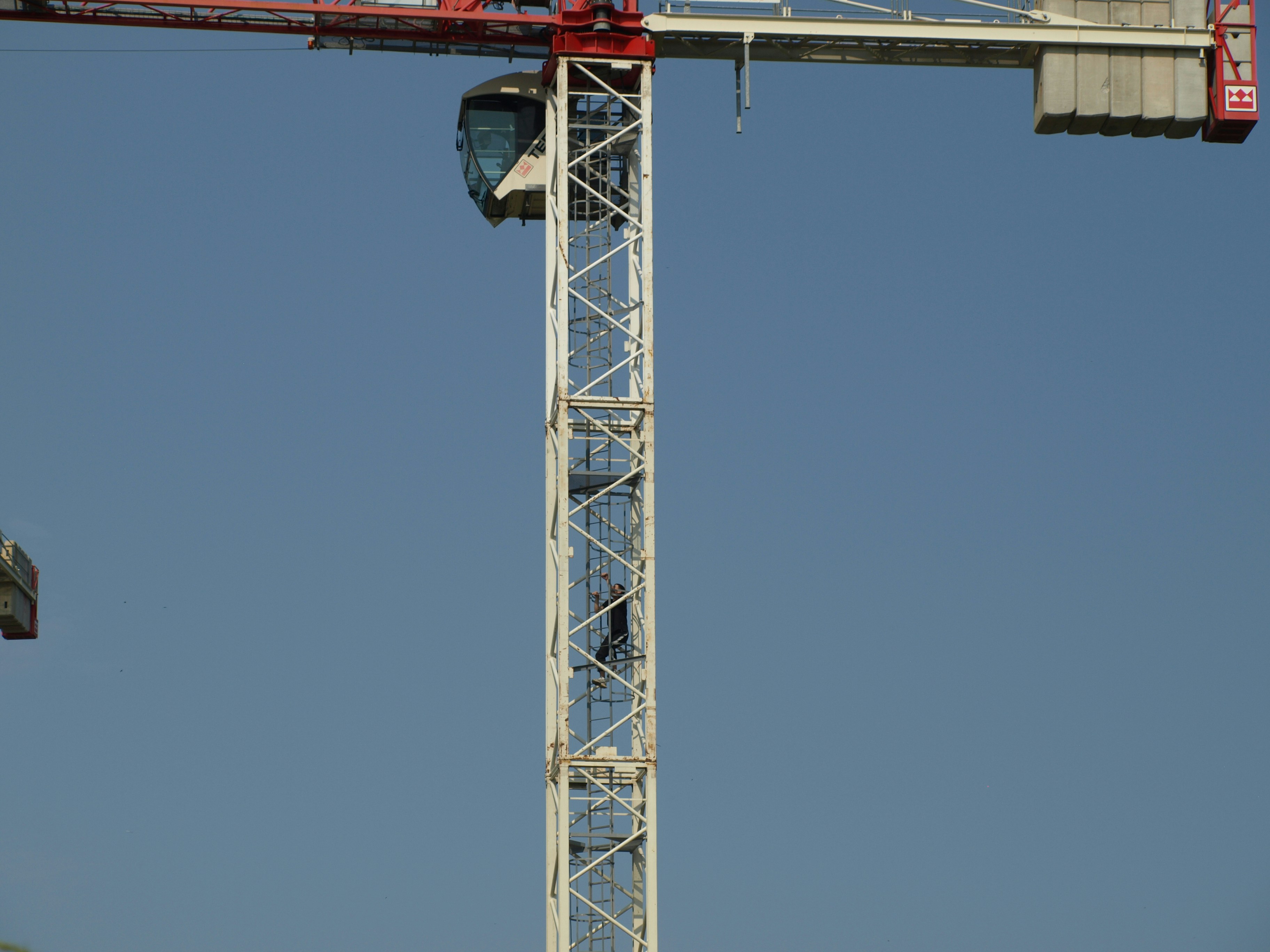 Tall construction crane rising into a clear blue sky with a portion of the jib visible; industrial structure framed against expansive negative space.