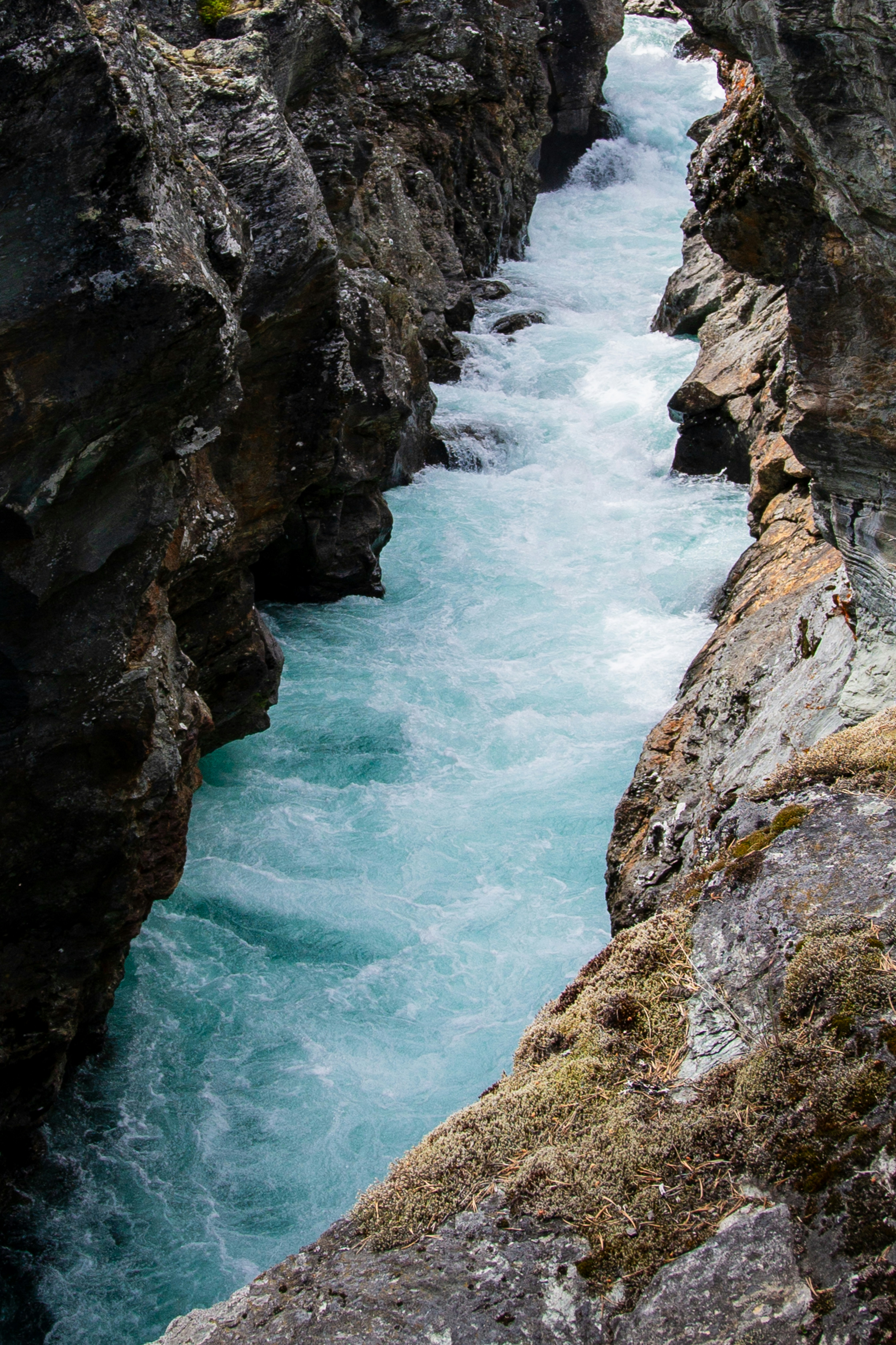 Turquoise river cuts through a steep rocky gorge, water rushing between rugged basalt walls in a narrow canyon.