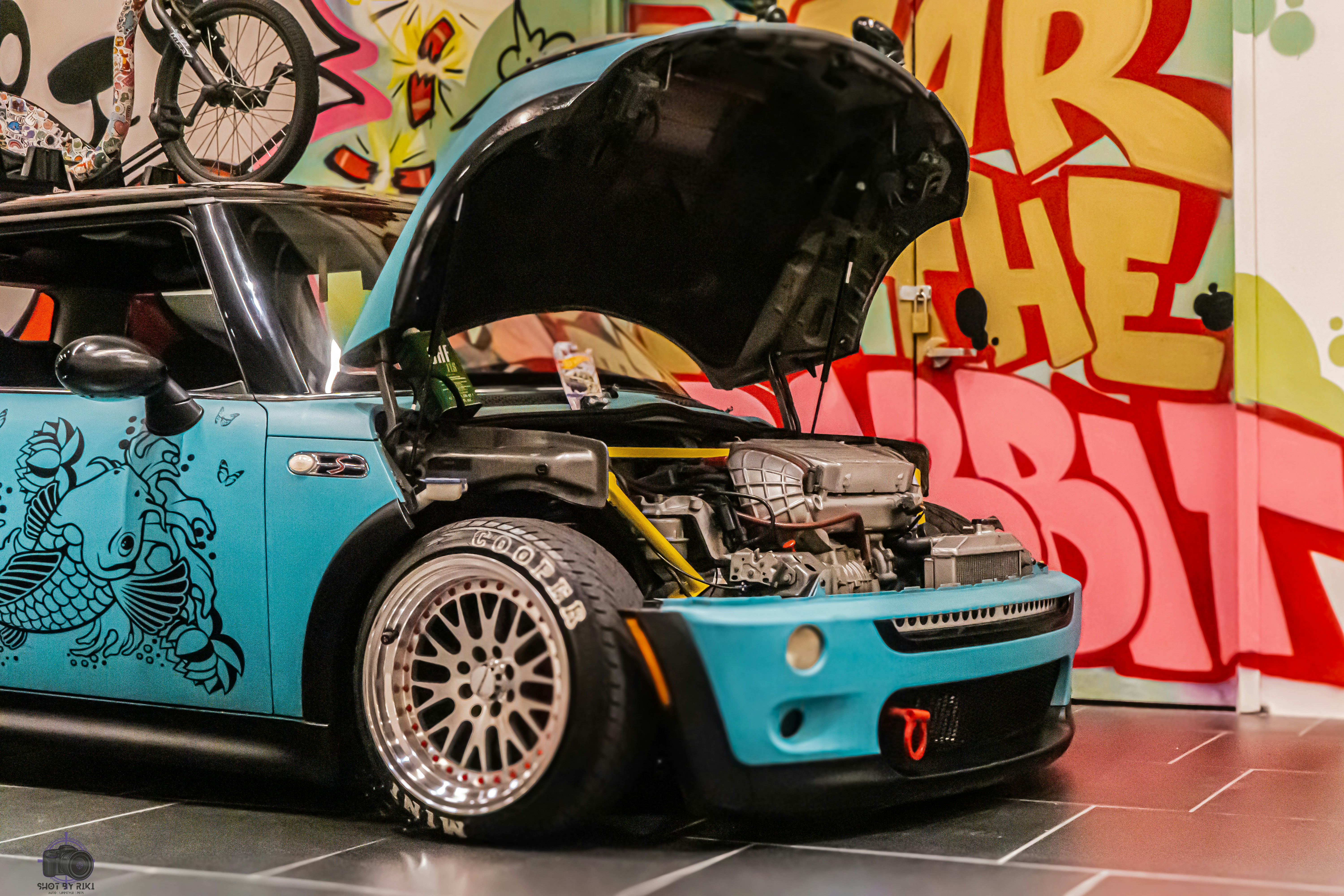 Vibrant teal classic with open hood in an urban mural backdrop