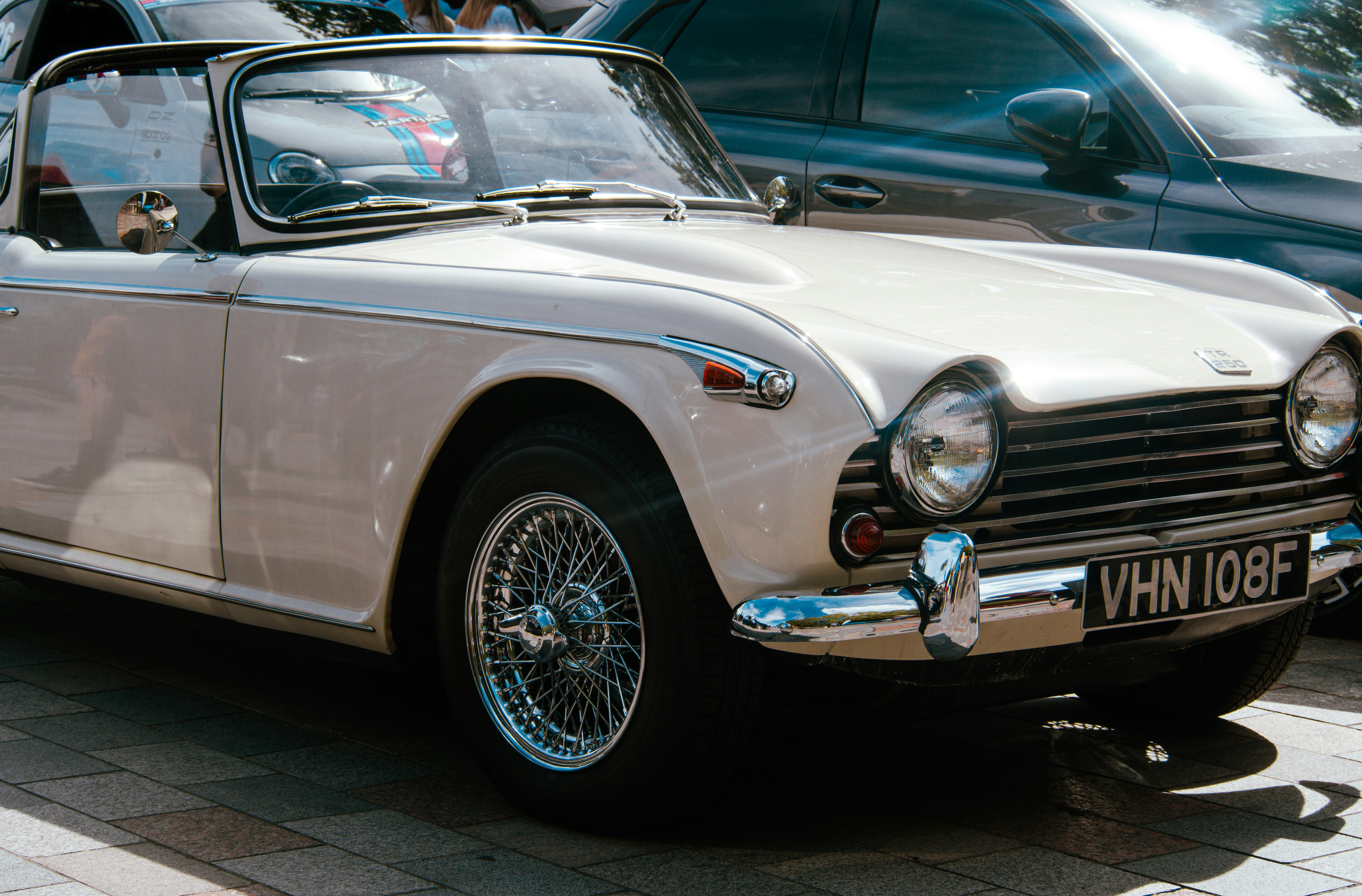 Cream-colored classic convertible parked on a street, chrome bumper and wire wheels catching the light; the car's front and license plate dominate the frame. This is a photograph of a vintage automobile, not a drawing or painting.