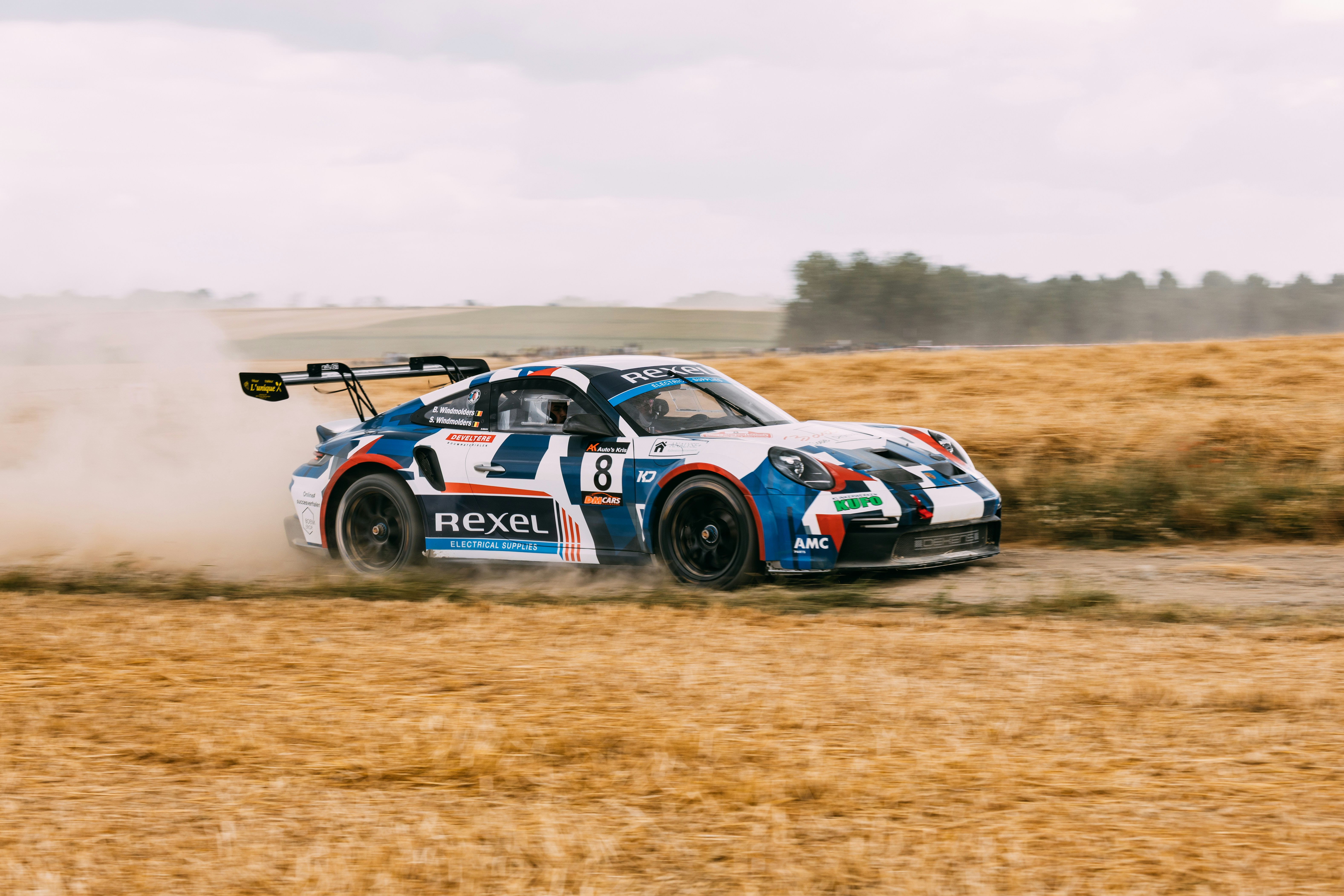Blue-and-White Rally Car Leans into a Dusty Field Across a Golden Harvest Plain