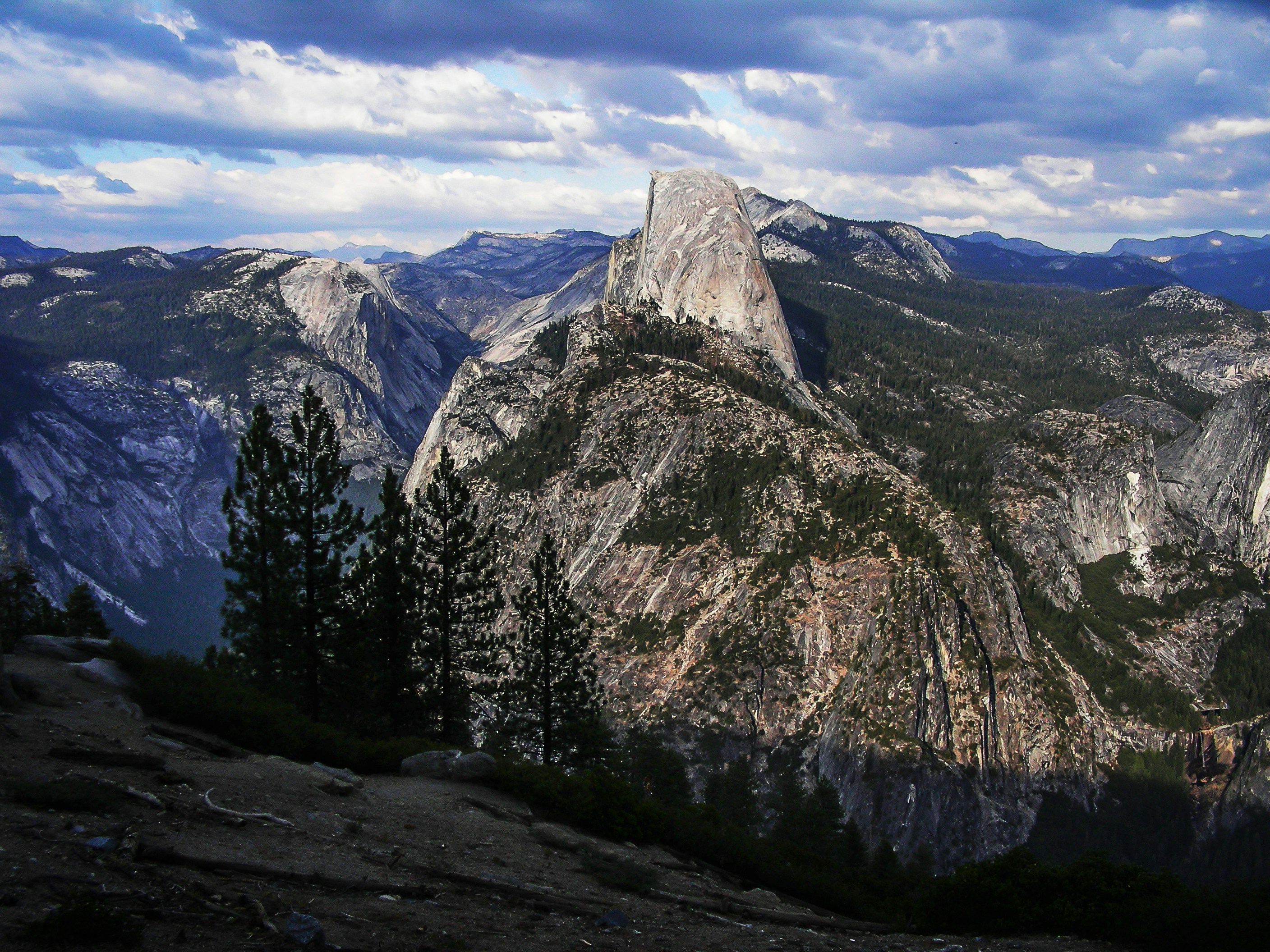 Iconic half dome mountain peak dominates a vast, cloudy landscape.