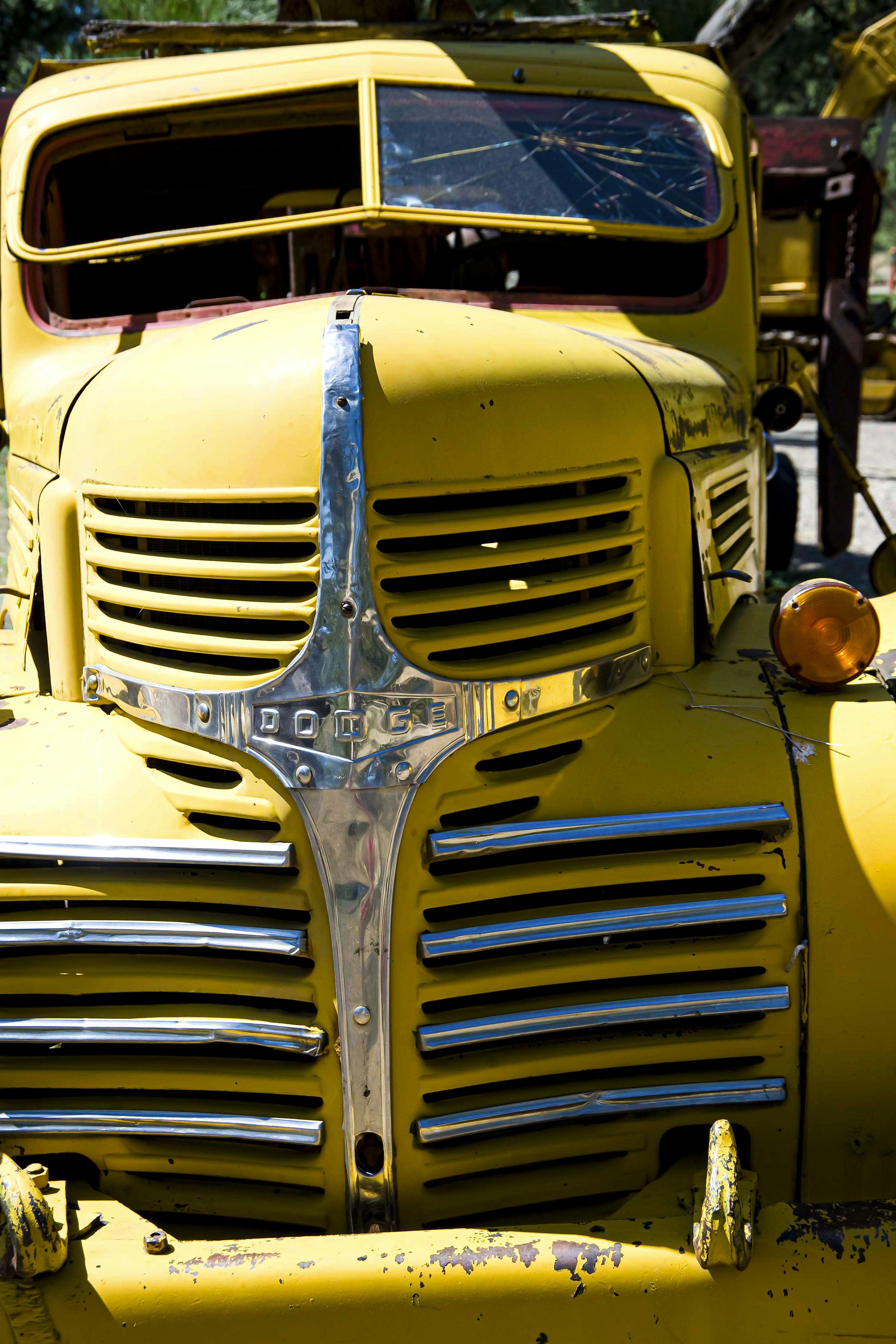 Close-up of a weathered yellow vintage truck, chrome accents and chipped paint catching sunlight; the scene emphasizes texture and a sense of nostalgia.
