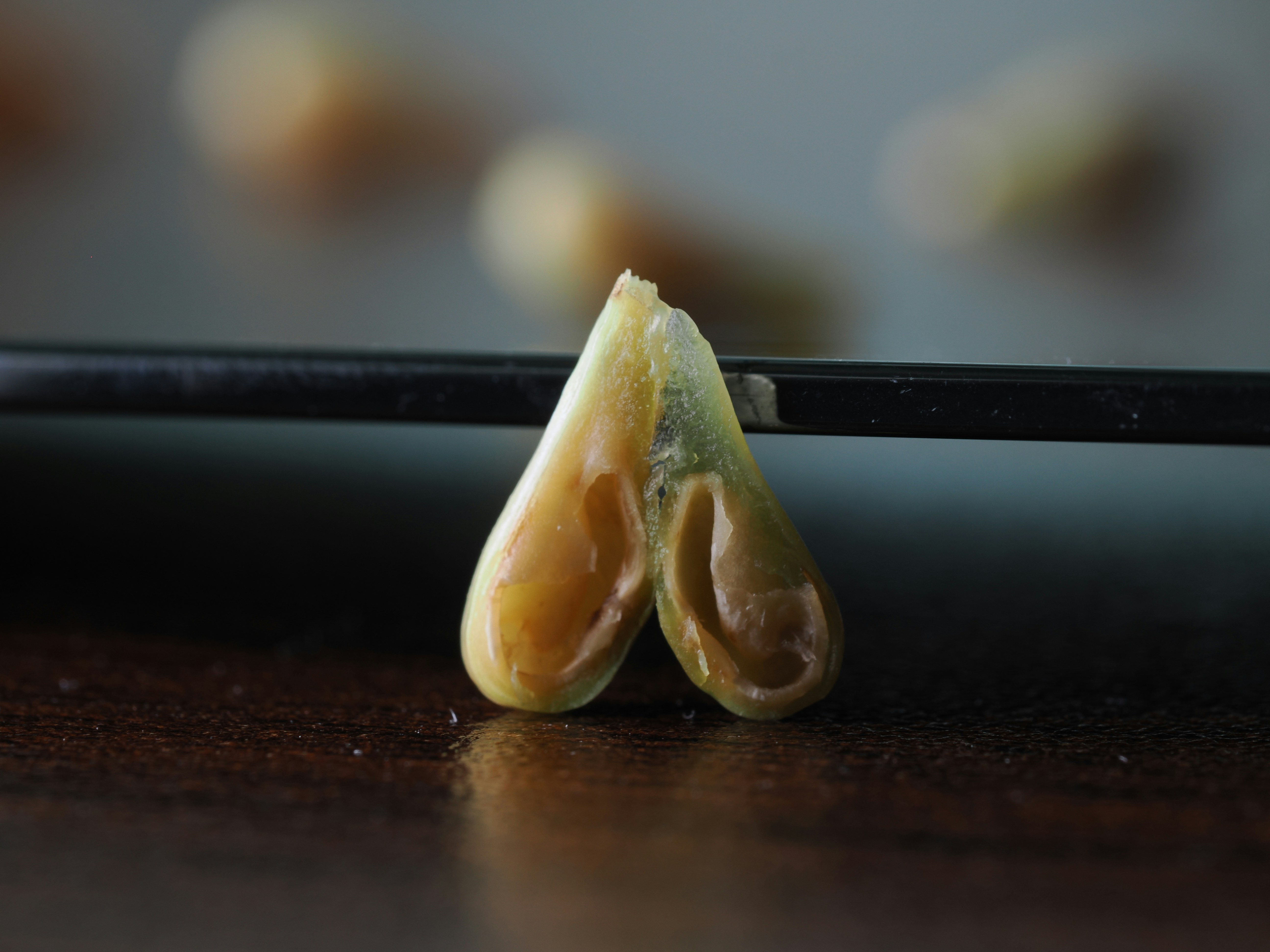 Two pistachios stand upright on a wooden surface with a glass strip in the background, emphasizing texture and color; a food close-up suitable for a culinary detail shot.
