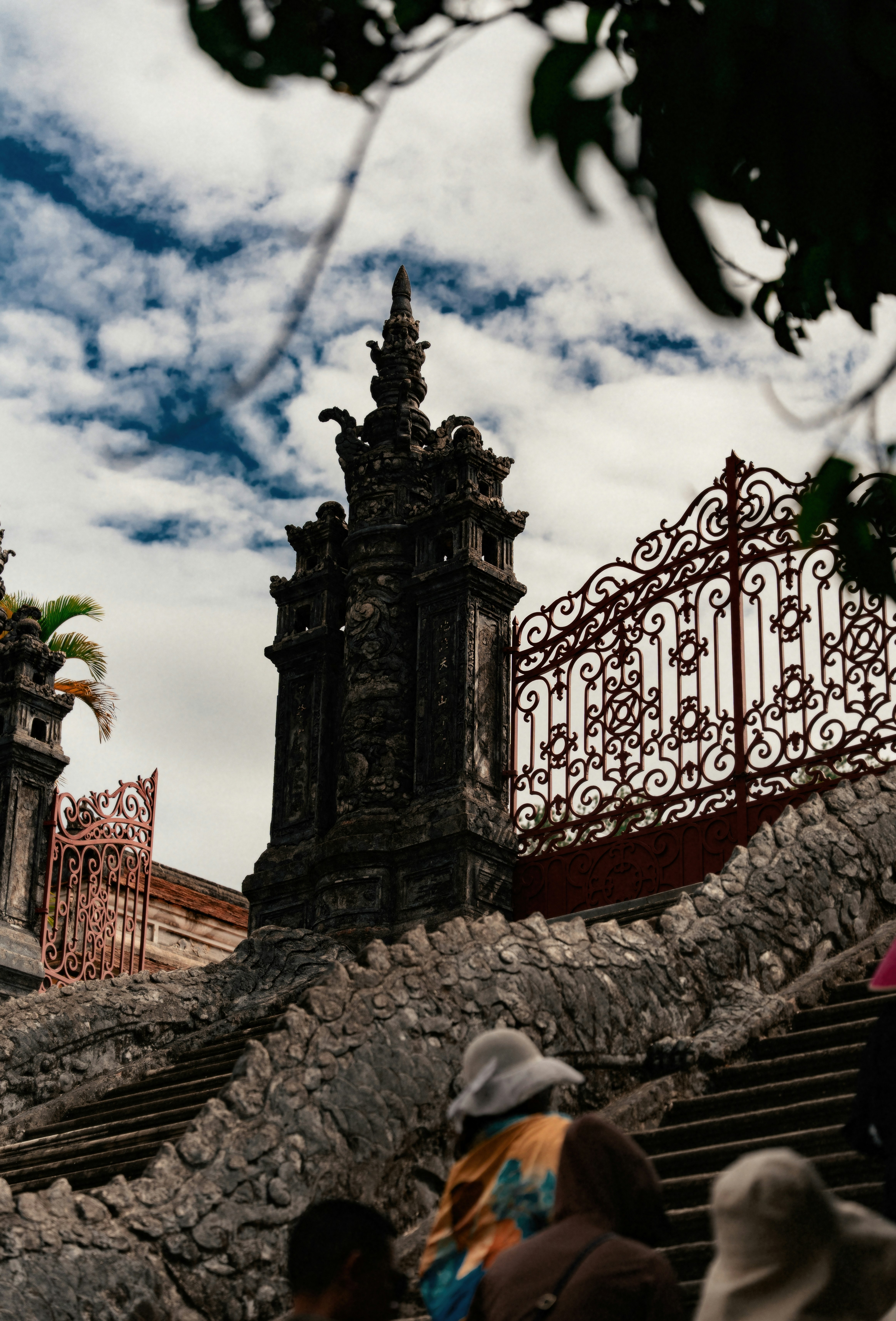 Stone Sentinel Above the Staircase: A Heritage Gate Framed by Sky and Scrollwork