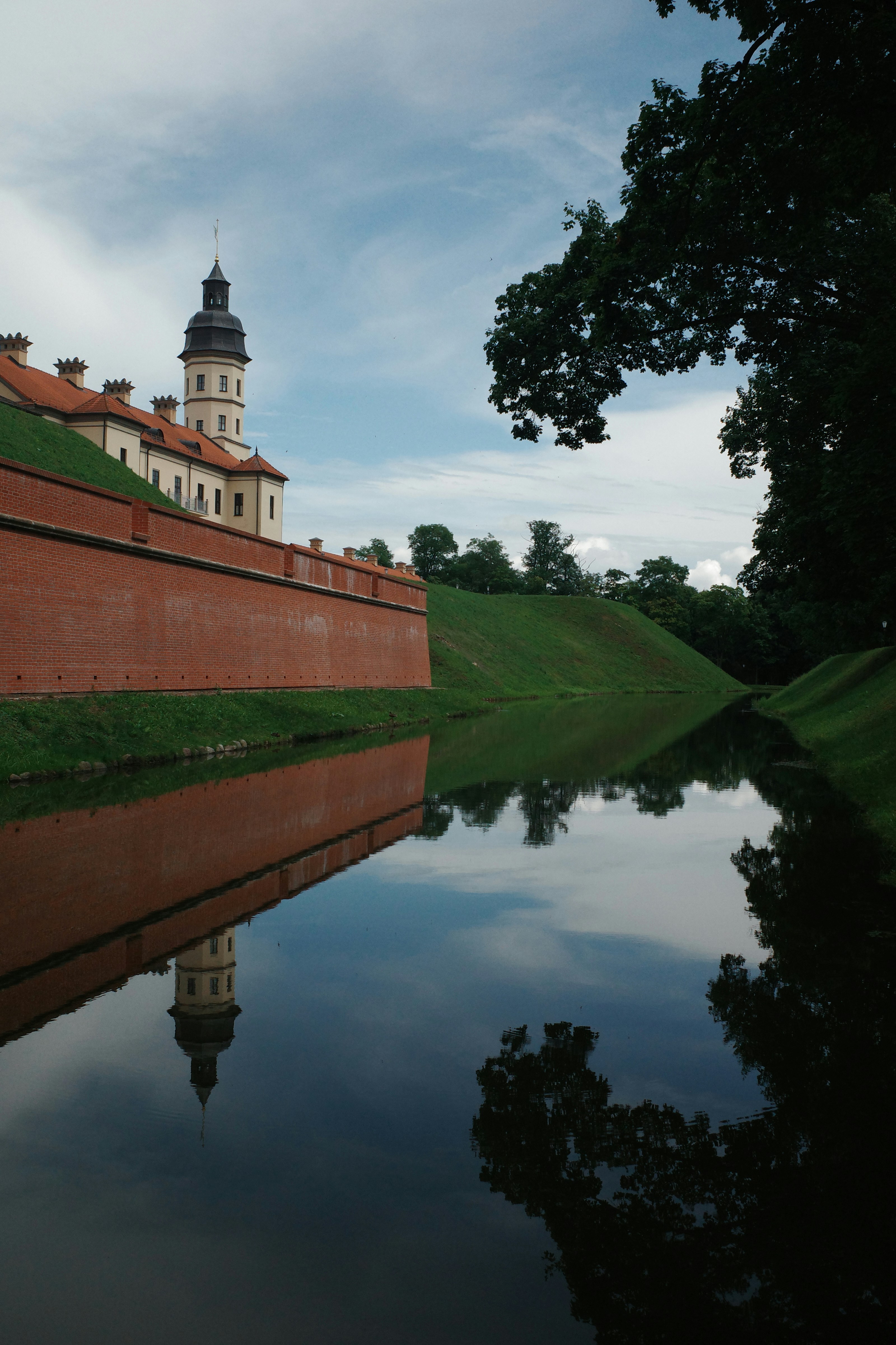 Reflected Fortress: Red Brick Wall and Lake under a Towered Skyline
