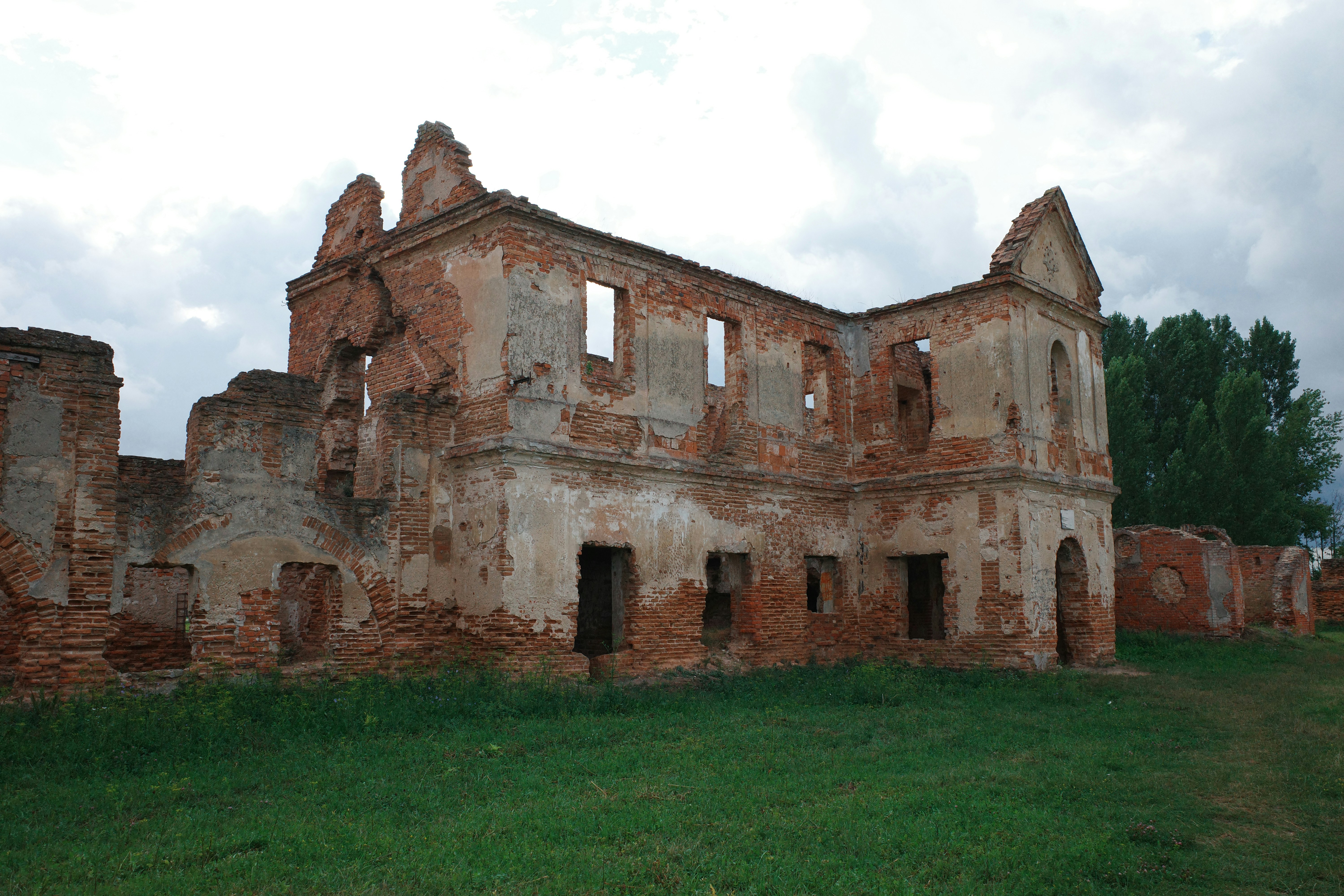 Ruins in Green Field: Weathered Brickwork Against a Cloudy Sky