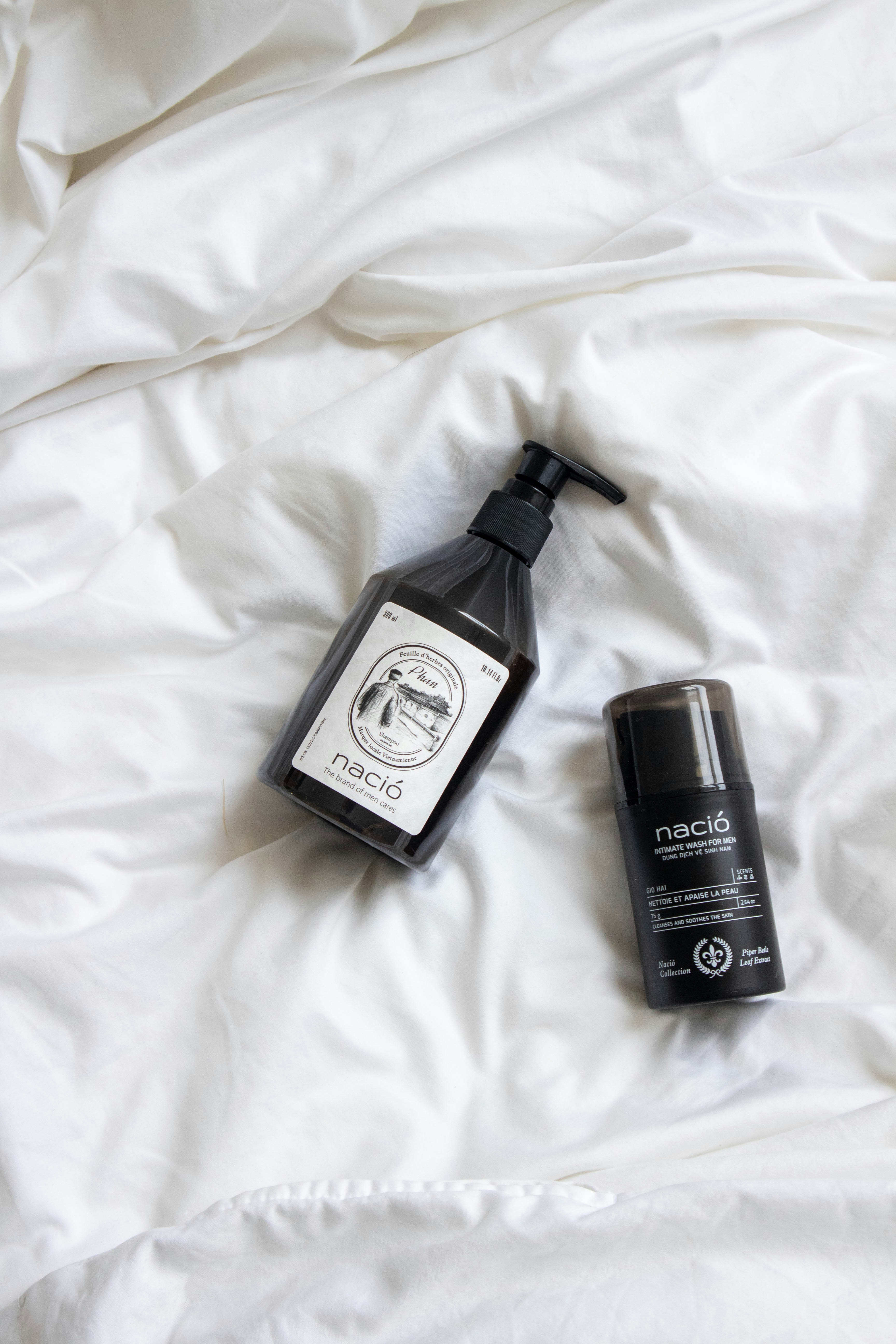 Dark shampoo bottle and soap pump resting on crumpled white bedding