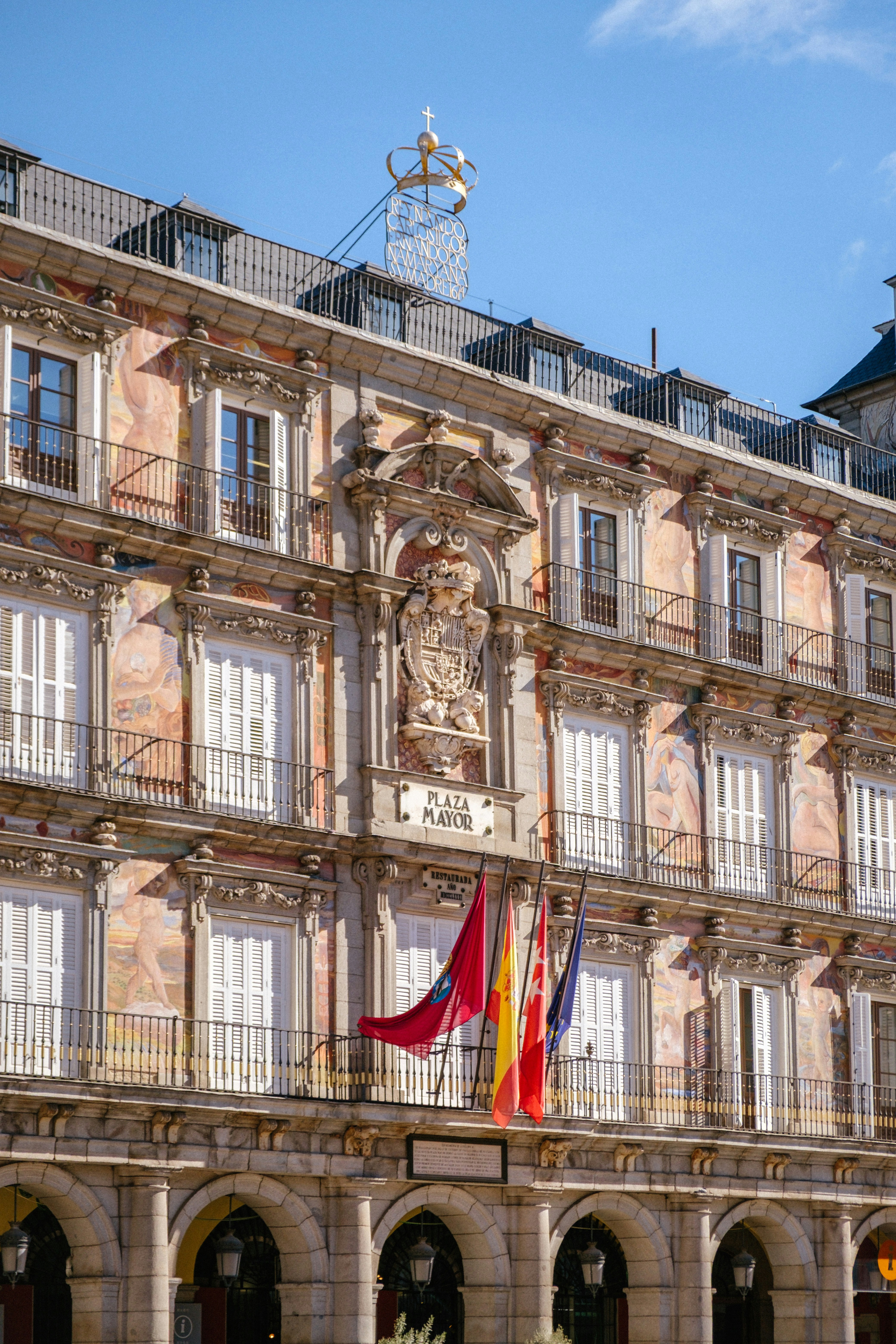Facade of Plaza Mayor: Flags, Arches, and Painted Naves Under a Clear Blue Sky