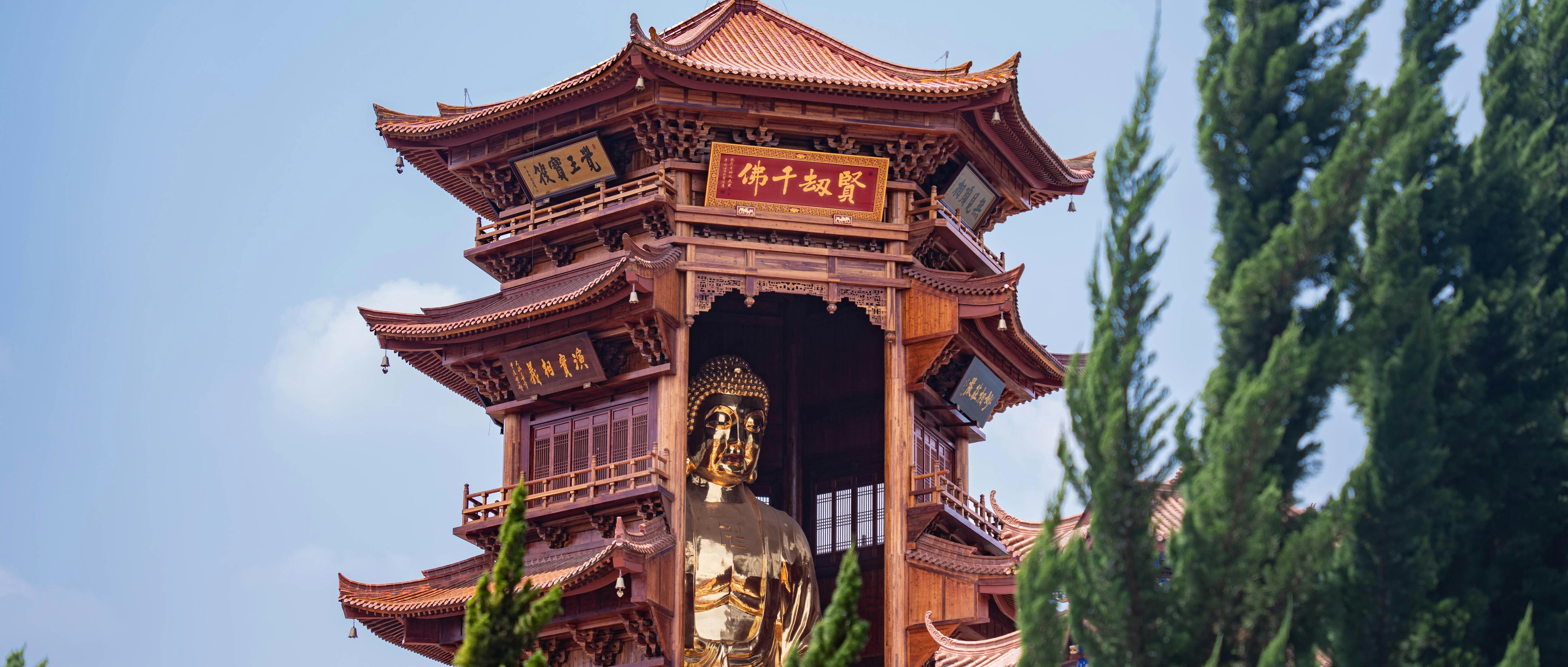 Golden statue framed by a traditional pagoda tower and surrounding evergreens, emphasizing architectural detail and cultural atmosphere.