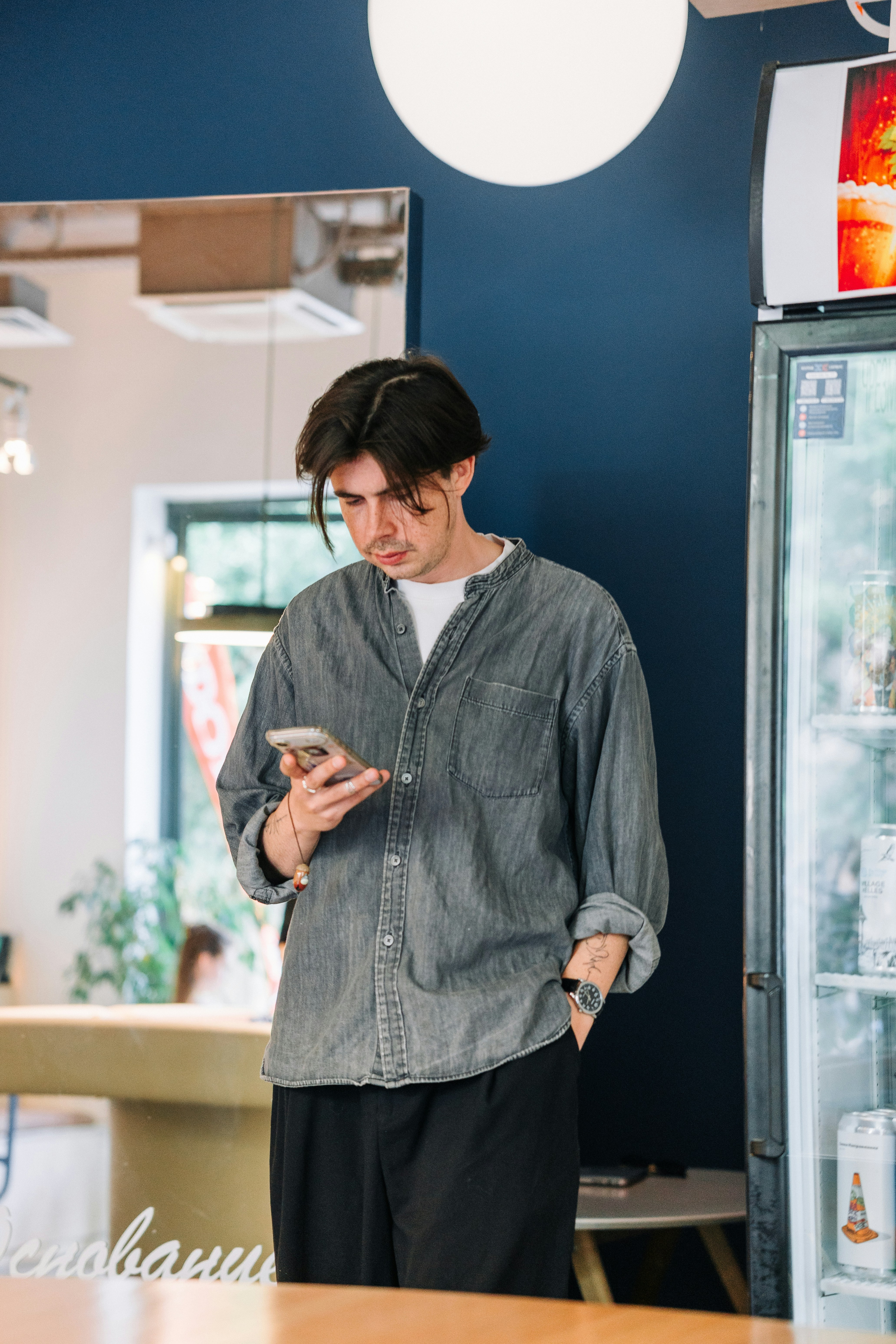 Softly Lit Moment: a man in a denim shirt checks his phone against a dark blue wall