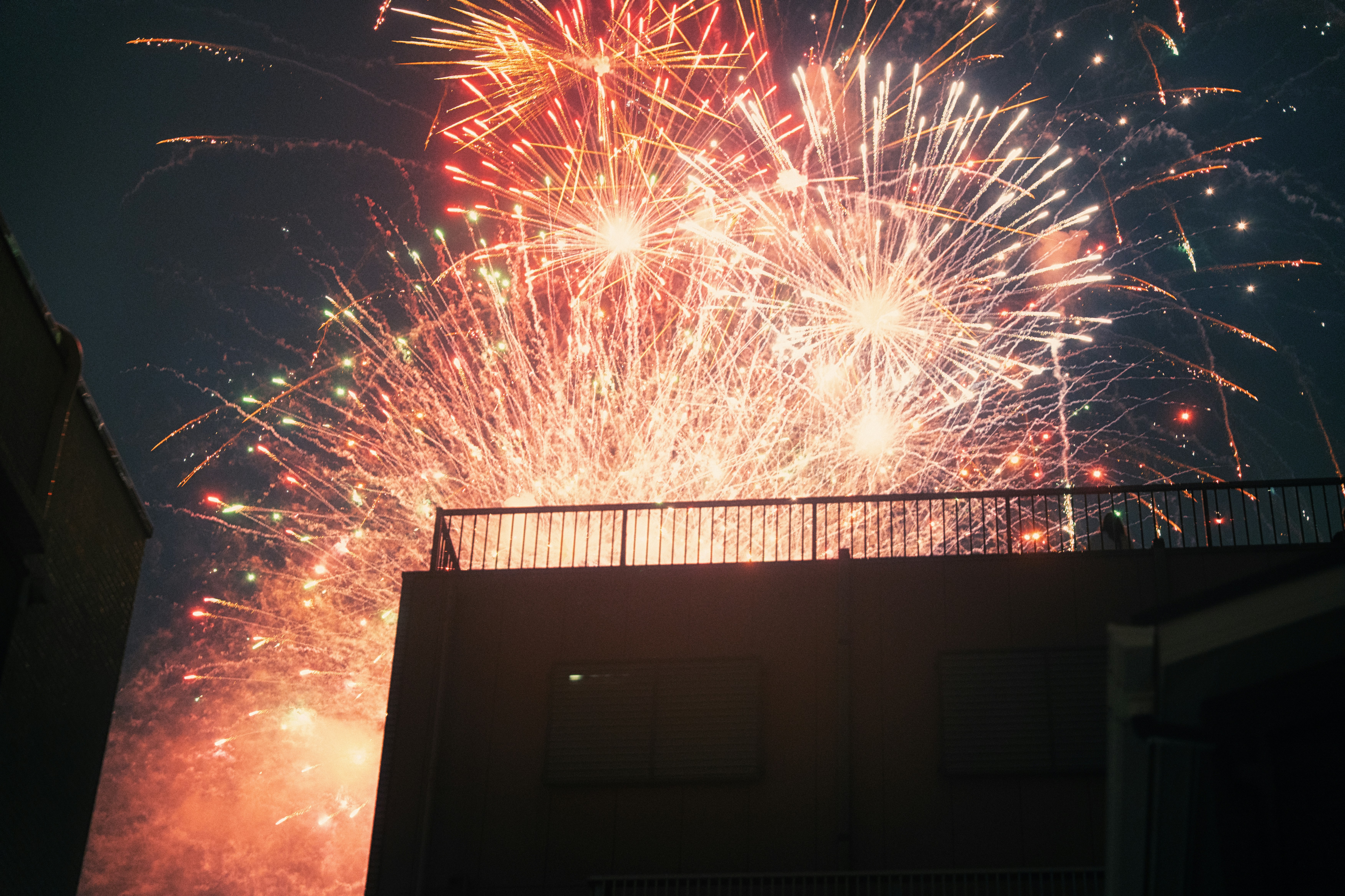 Skyfire over the Rooftop: Night Burst Above the Silhouetted Building