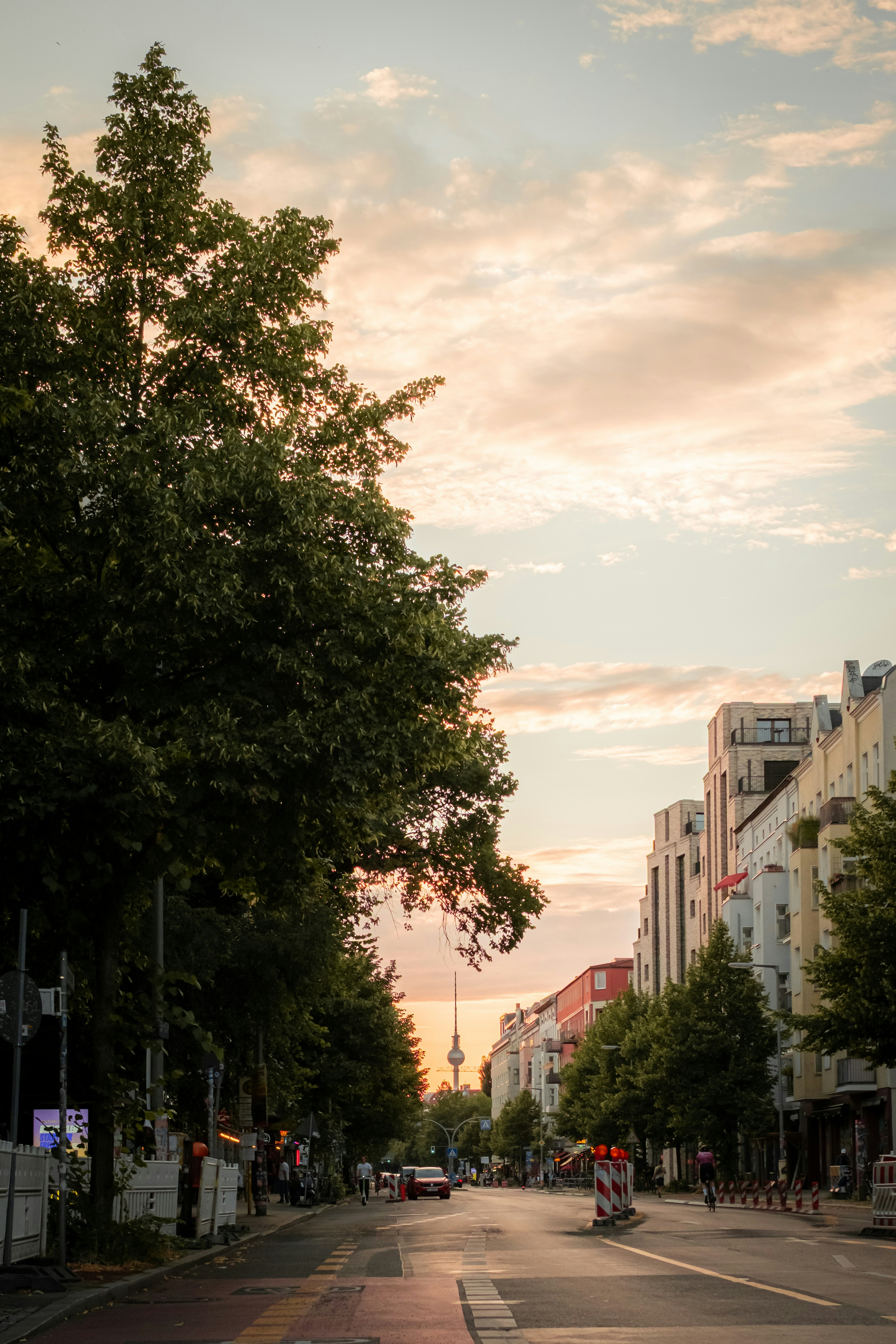 Warm sunset light washes a quiet urban avenue lined with trees and buildings, guiding the eye toward a distant spire along the horizon.