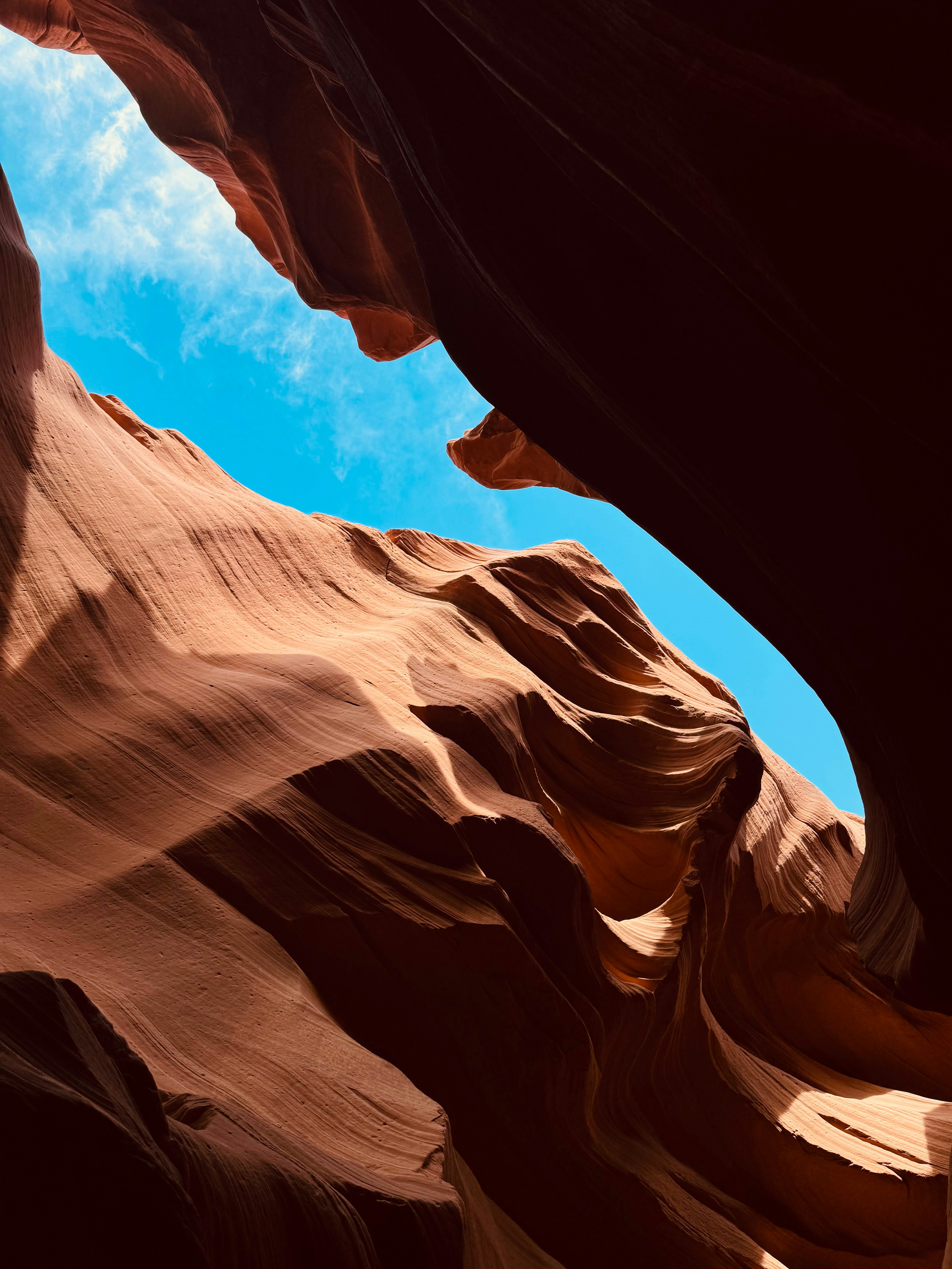 Sculpted red canyon walls curl inward to reveal a vivid blue sky, emphasizing natural erosion patterns. This landscape captures the contrast between shadowed rock and bright sky.