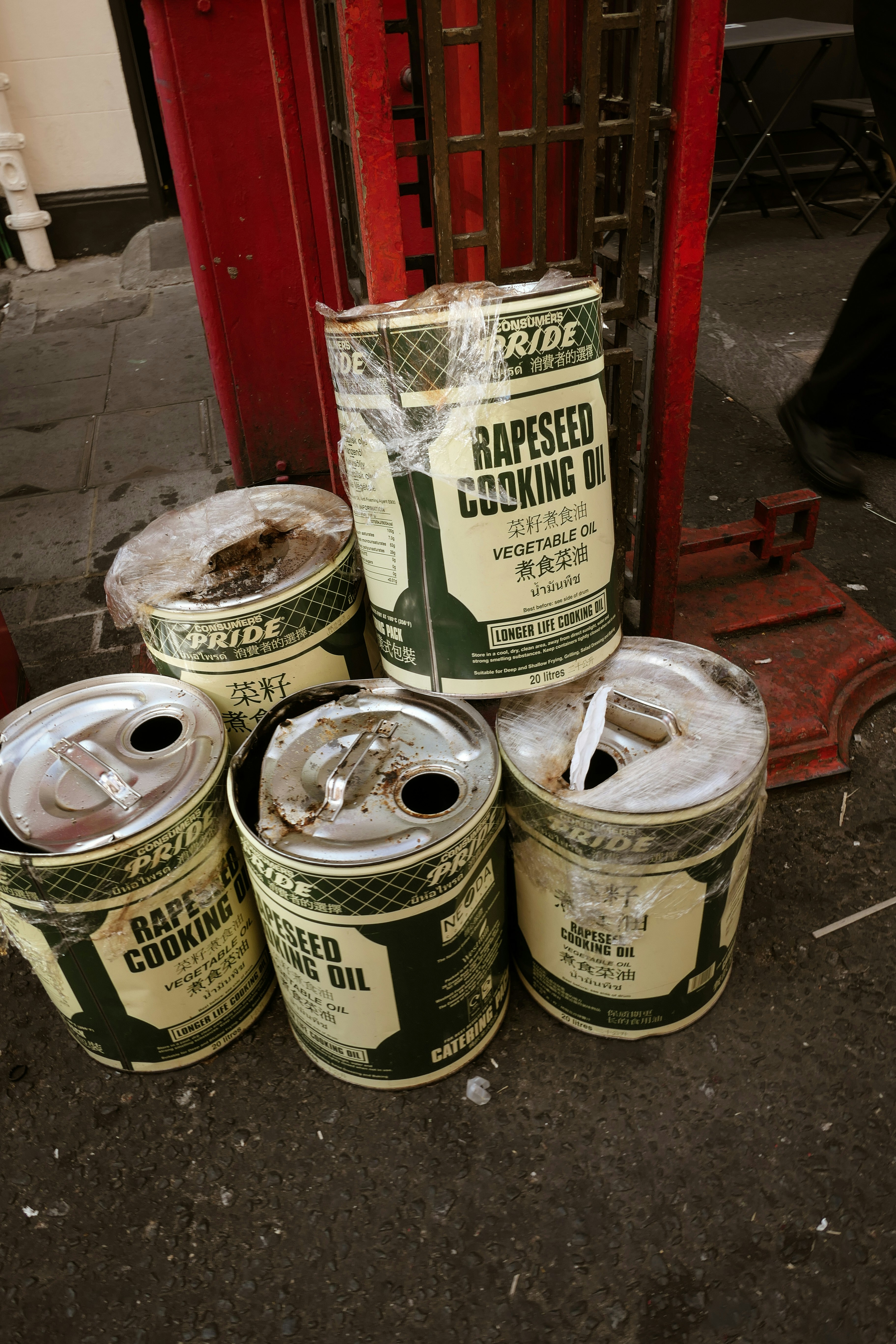 Street-side Drip: Vintage Oil Cans at a Red Door Threshold