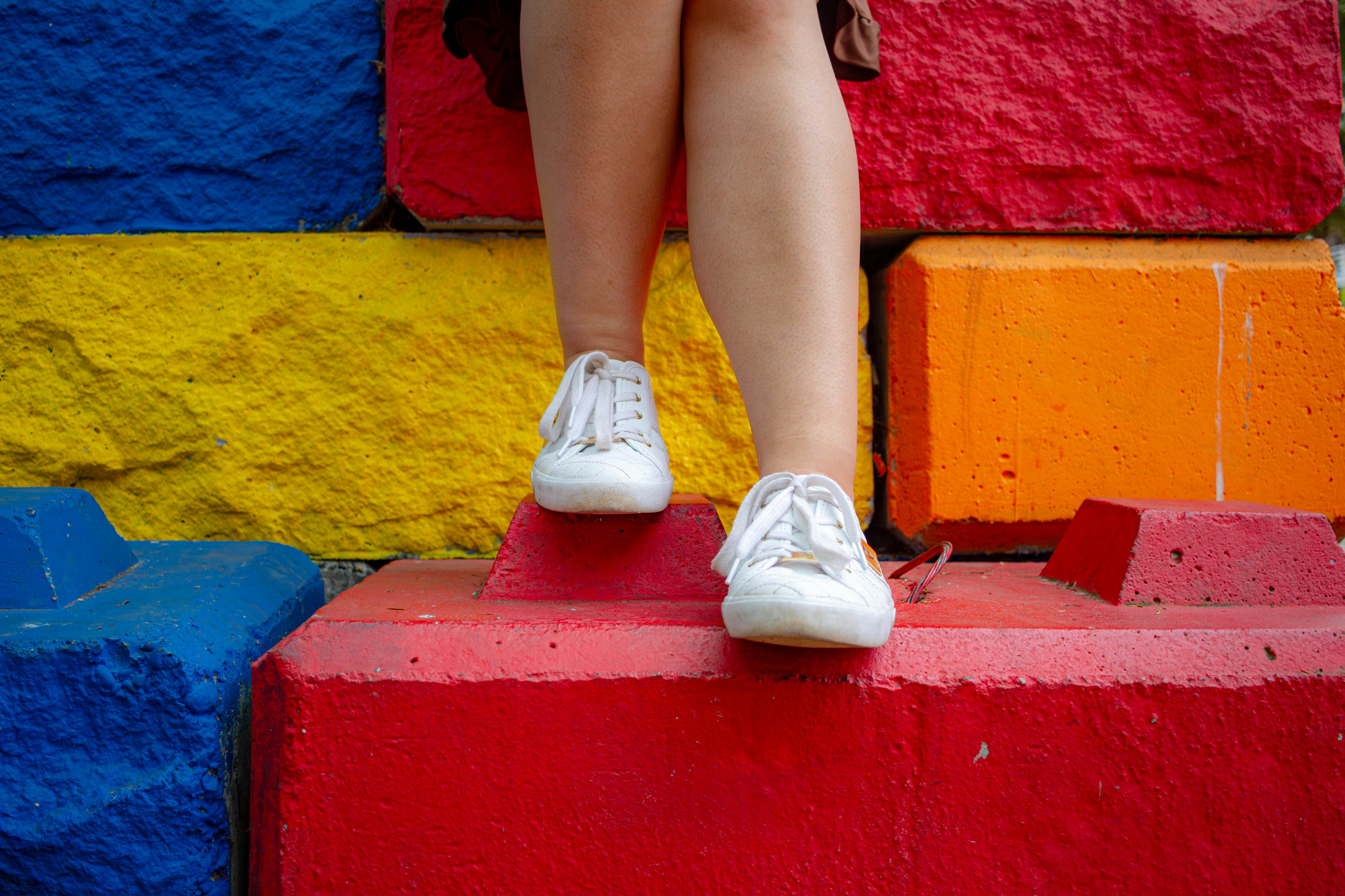 Steps into Color: A Child’s White Sneakers on a Rainbow Block Stairway