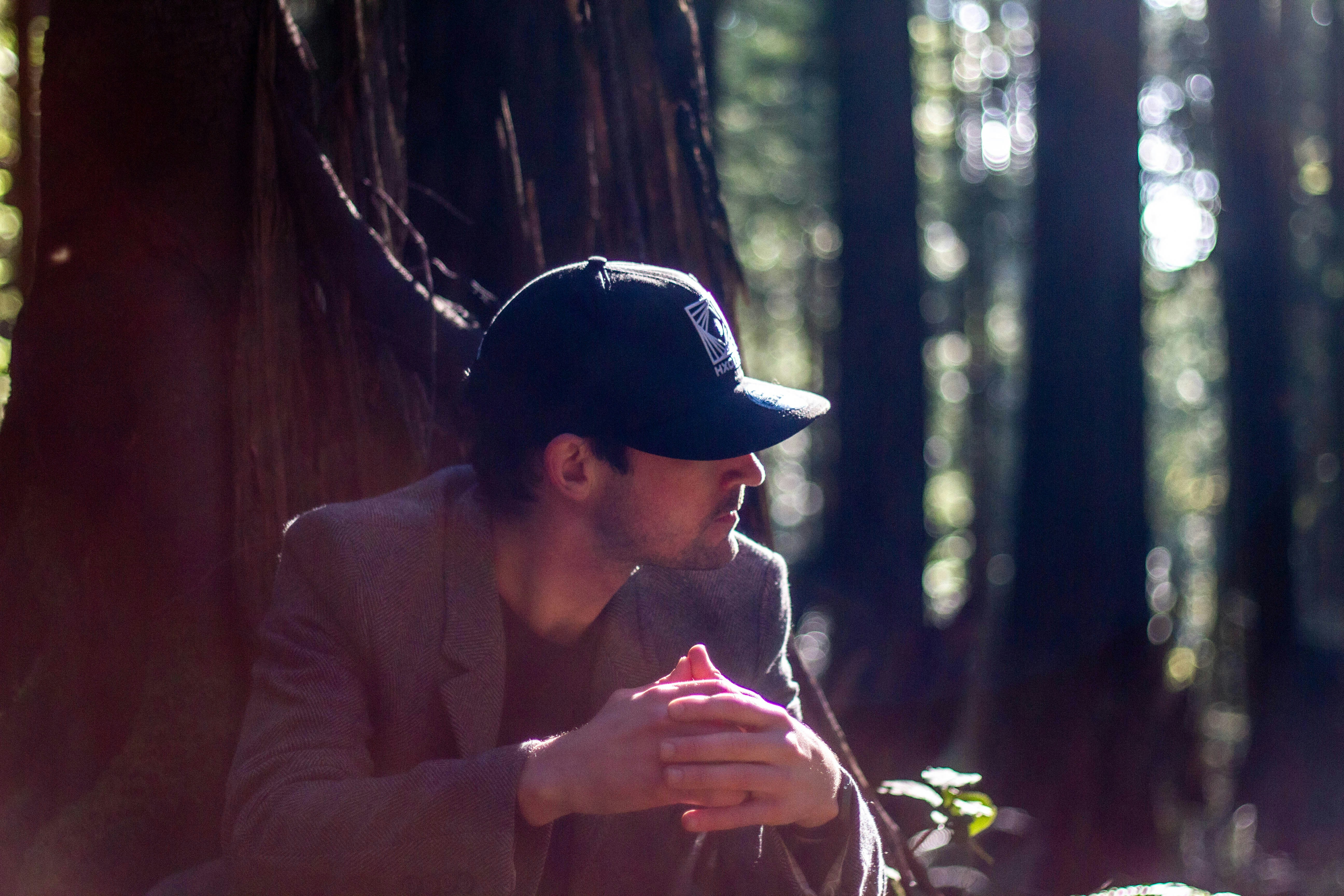Quiet contemplation under the pines: man in a cap shaded by a forest canopy