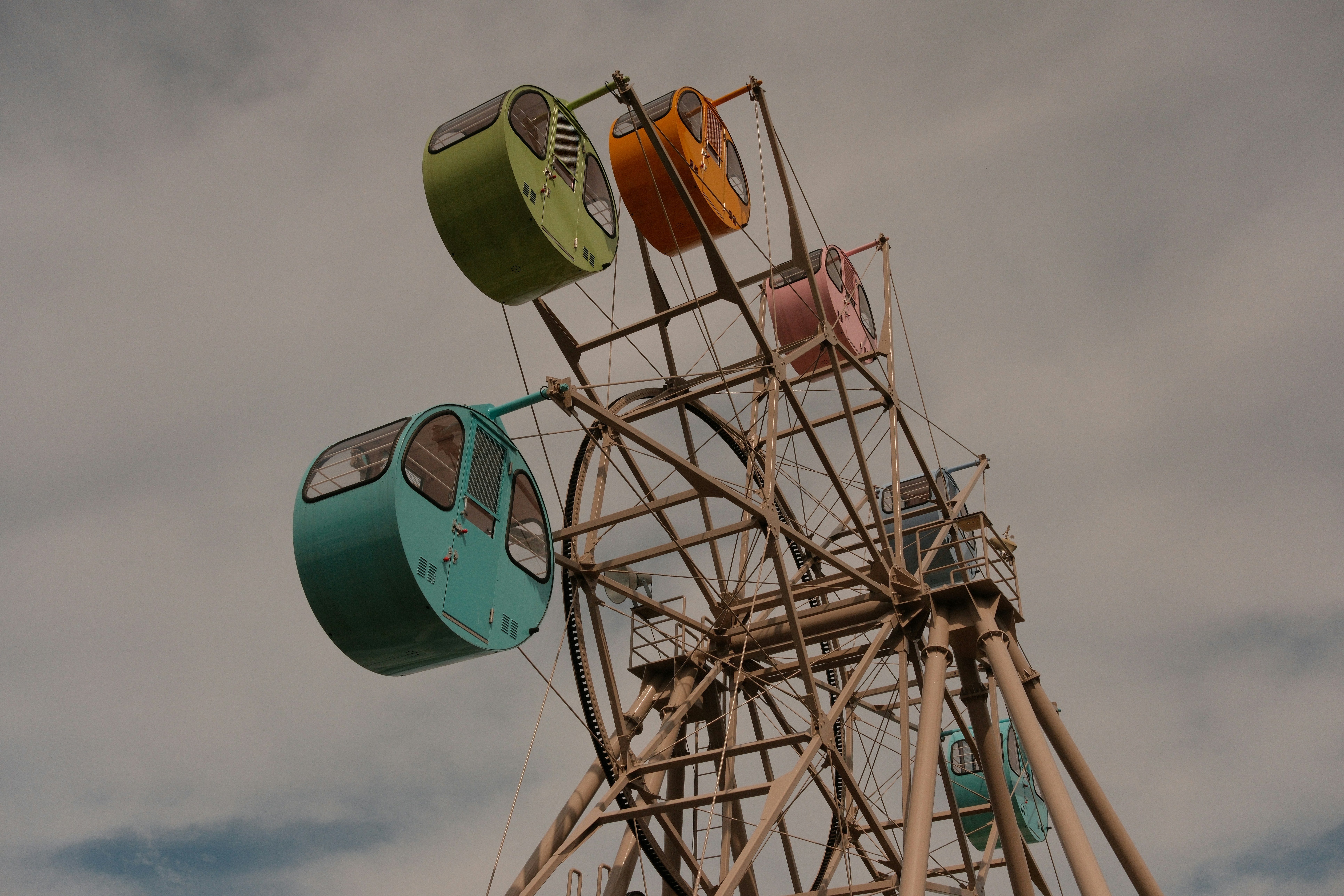 Vibrant gondola cabins hang from a weathered metal ferris wheel set against a soft, cloudy sky.