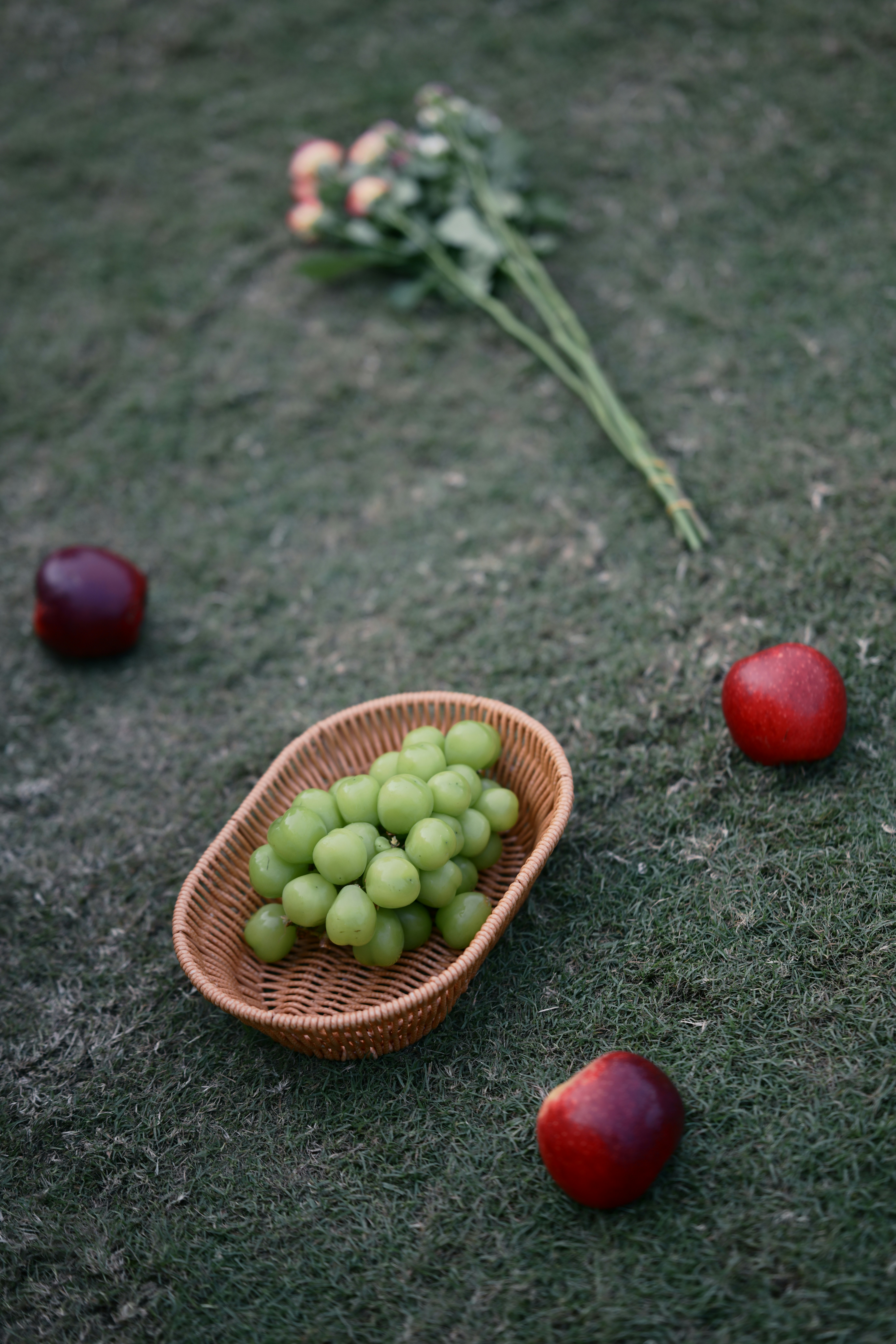 Basket of Green Grapes Set on Grass with Red Apples