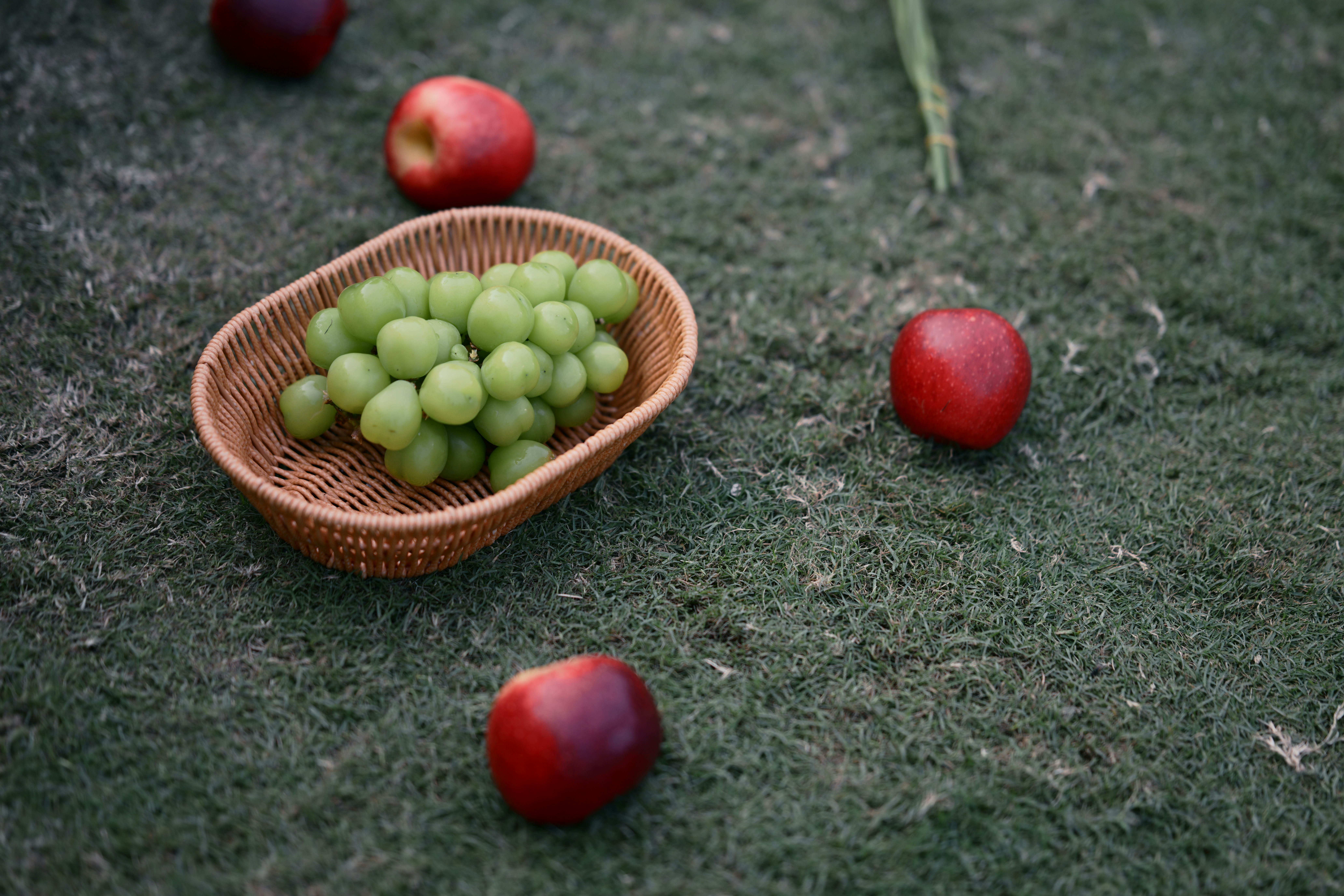 Basket of Green Grapes Among Red Orbs on Grass