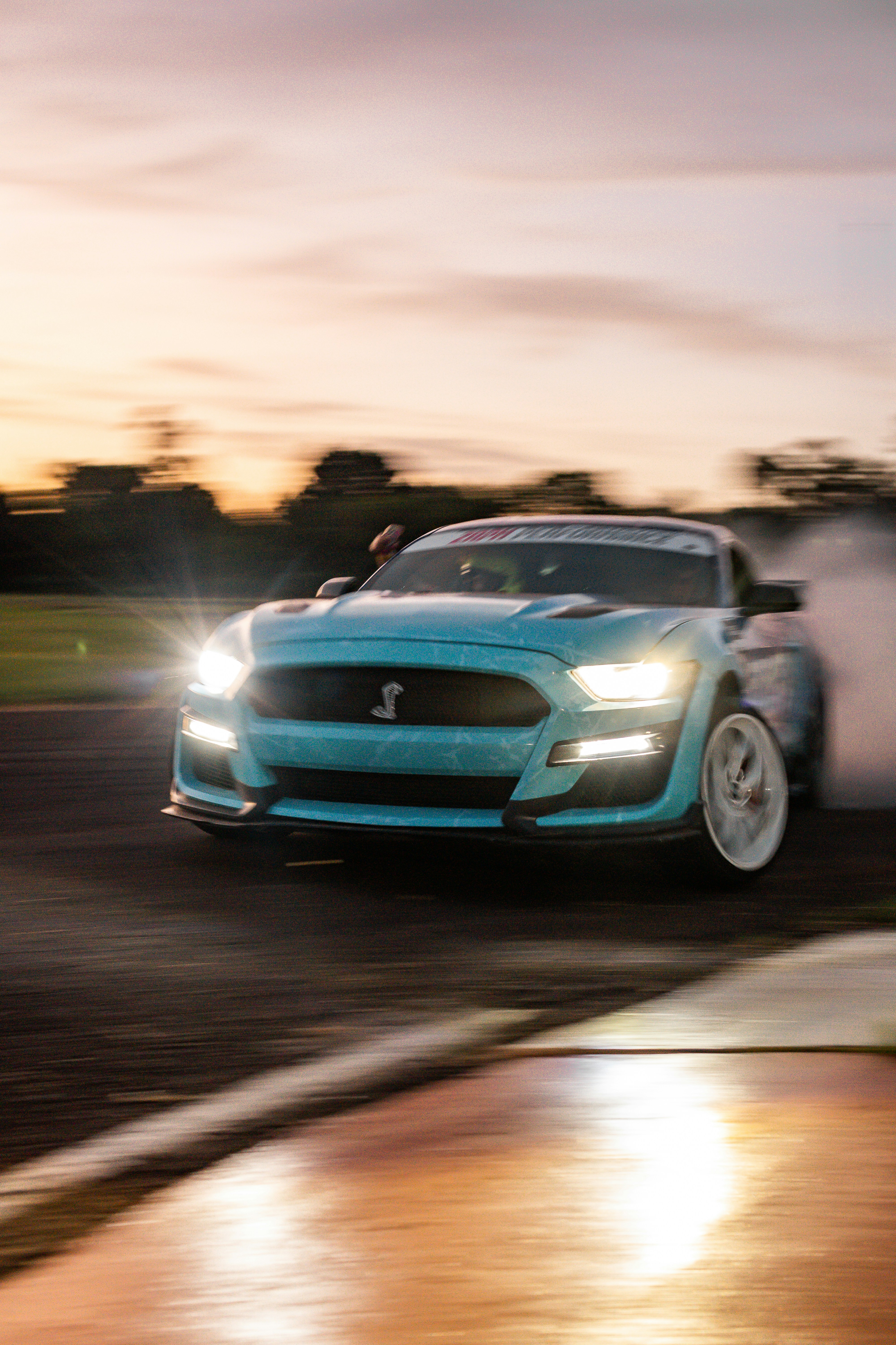 Sunlit Drift: Turquoise Mustang Skims the Track at Dusk