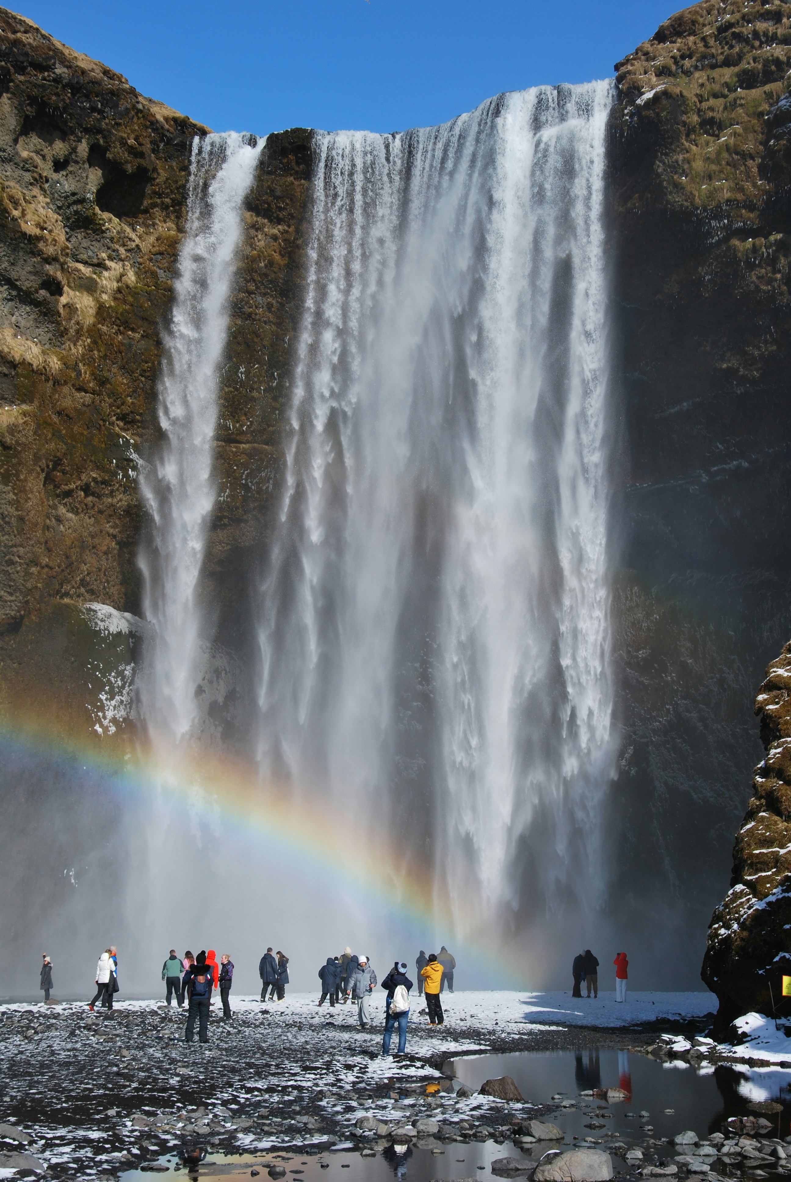 Rainbow at the Base: Visitors feel the Mist of Icelandic Seljalandsfoss Falls