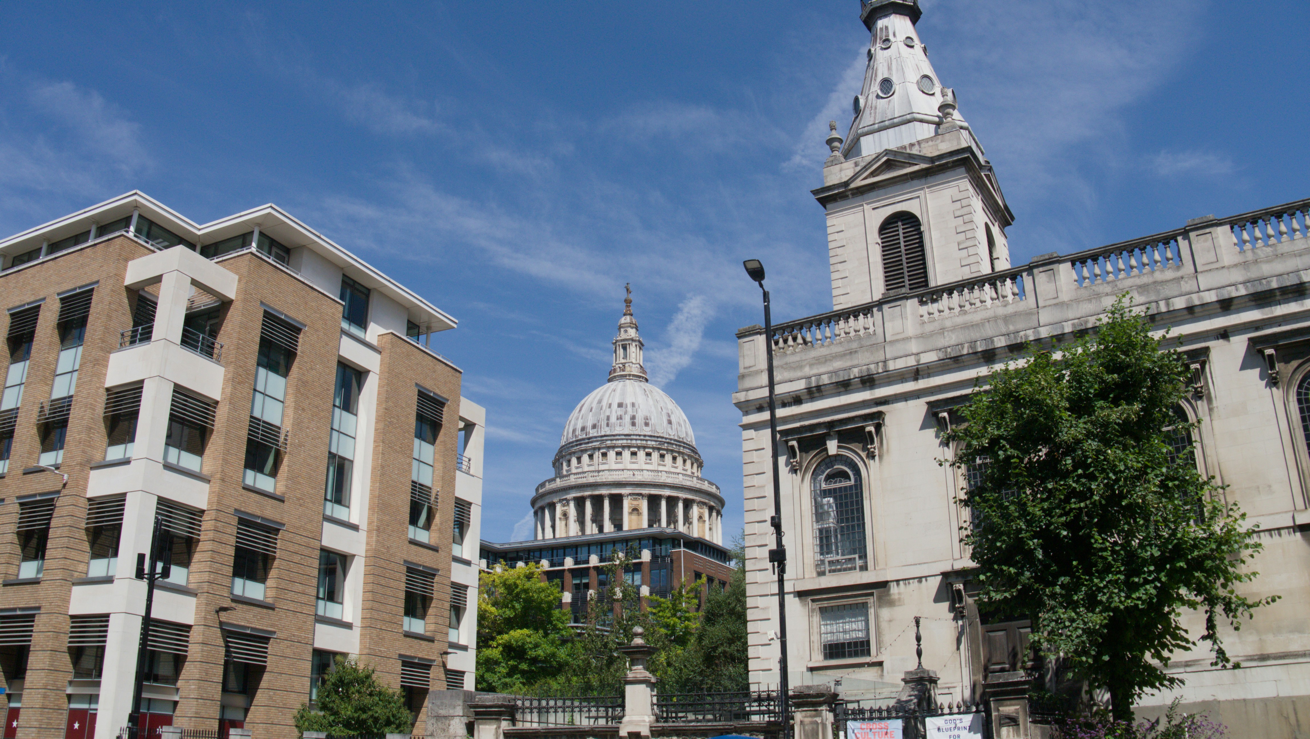 Bright cityscape with historic church, domed capitol, and modern building under a blue sky. Aiming to capture architectural contrast and street-level activity.