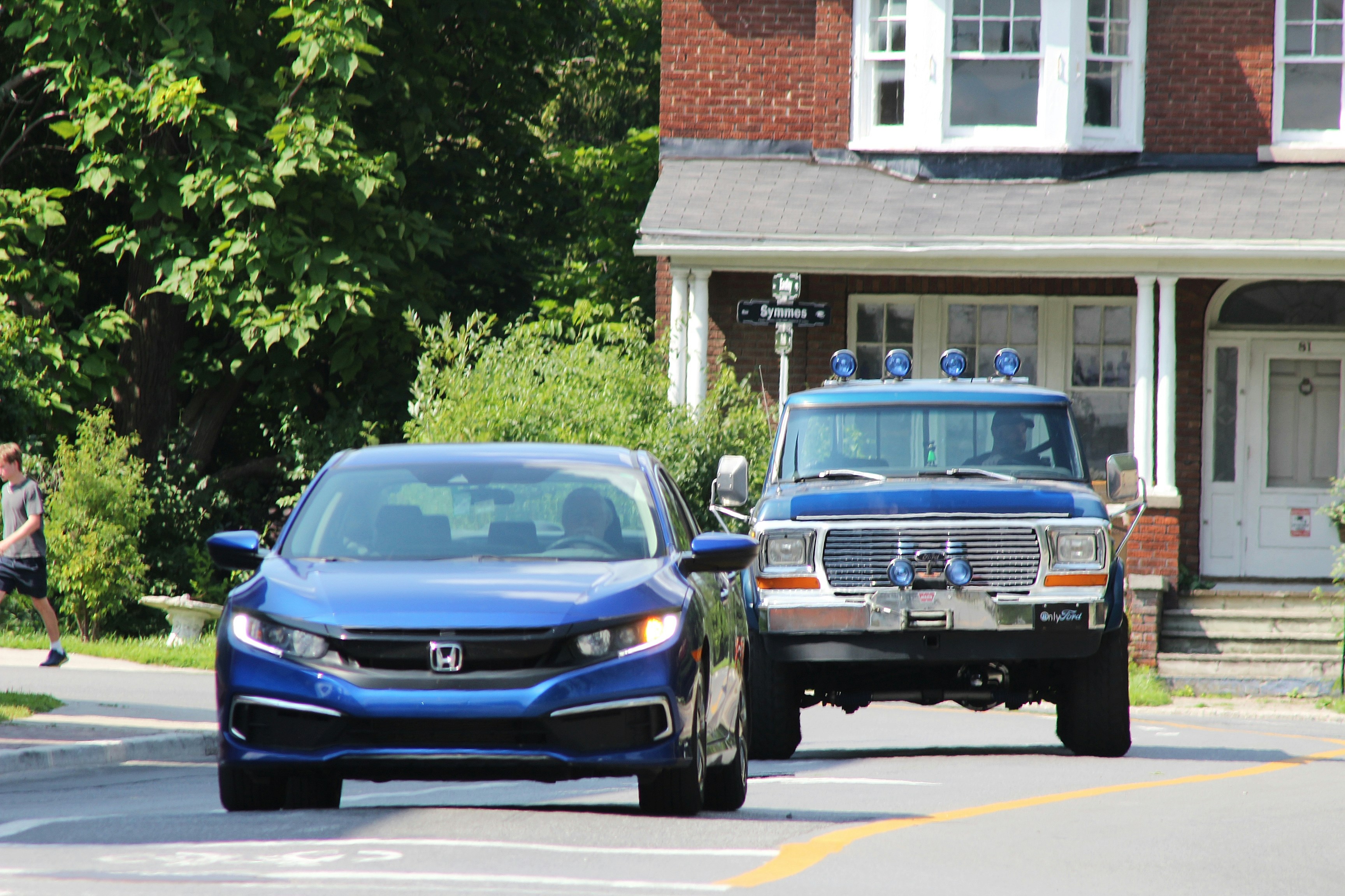 Blue sedan in pursuit of a vintage utility truck down a suburban street